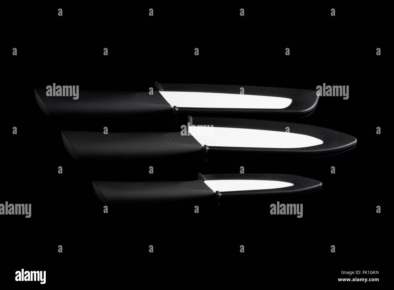 Set of three ceramic knives in black cover on black reflecting ...