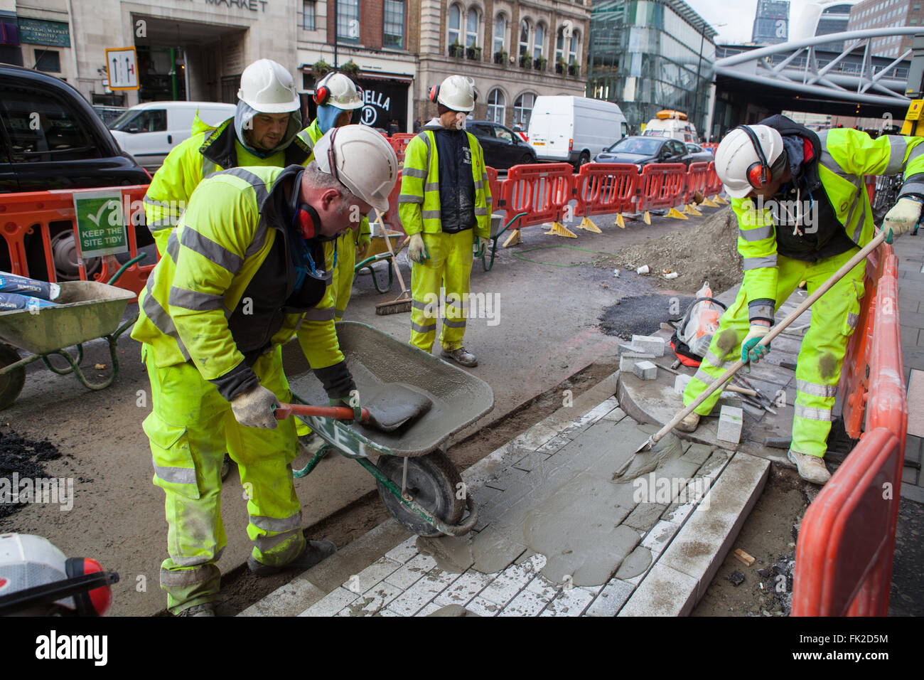 Workmen laying and spreading cement on a pavement and road in London ...