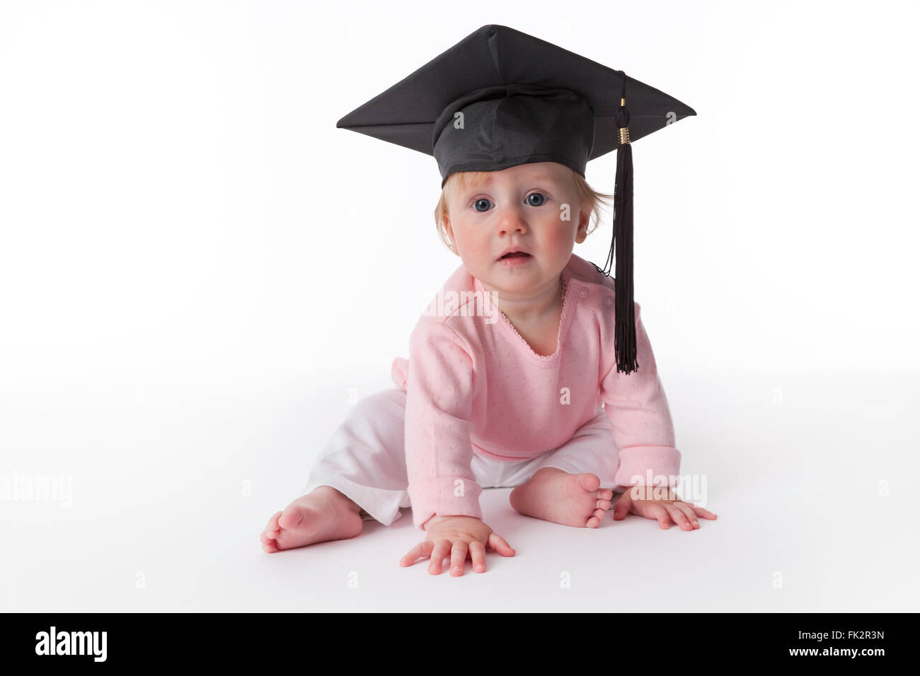 Baby girl is sitting on the floor with a graduation cap on white ...