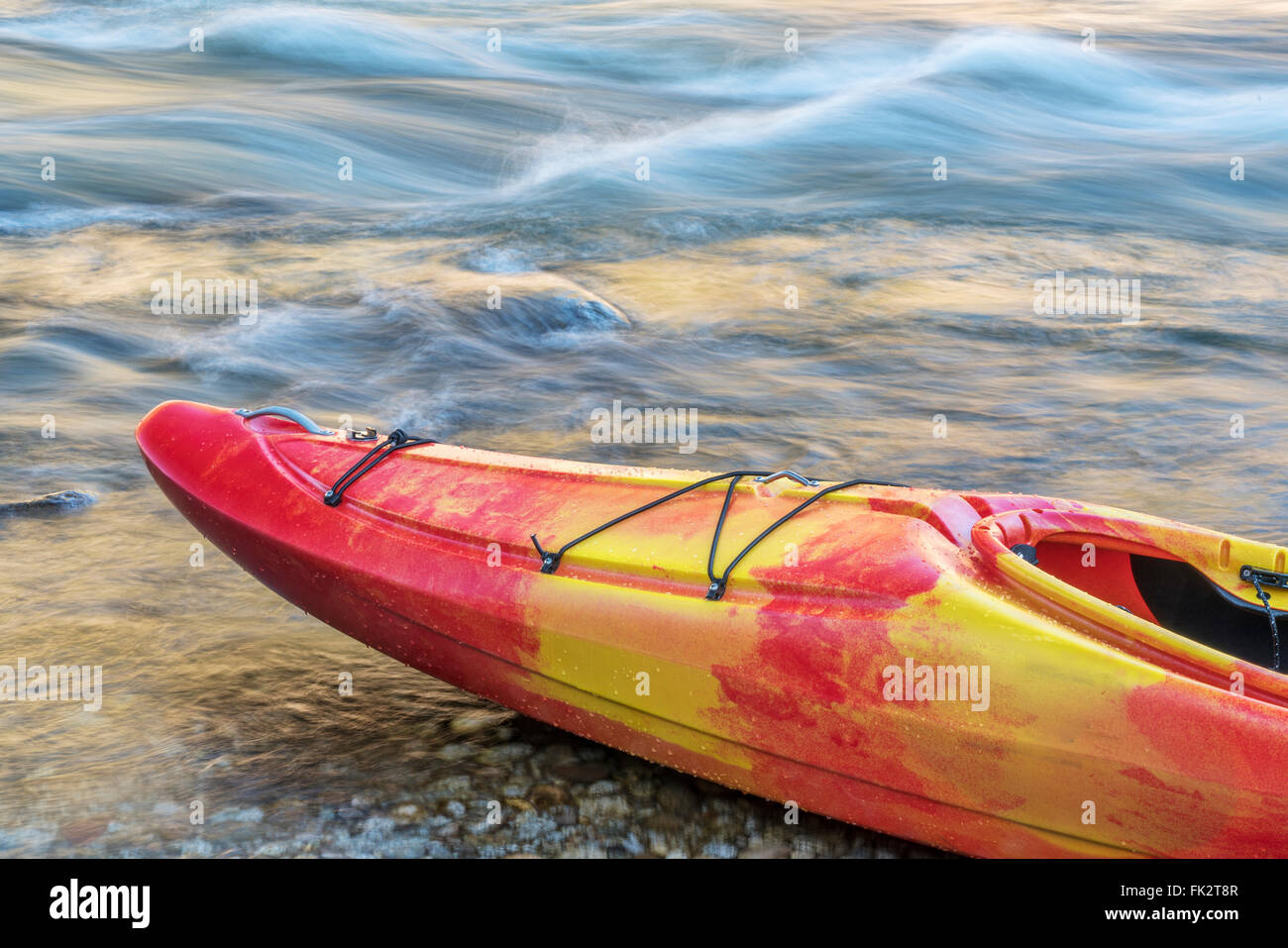 Bow of whitewater kayak on a river shore with a rapid in background ...