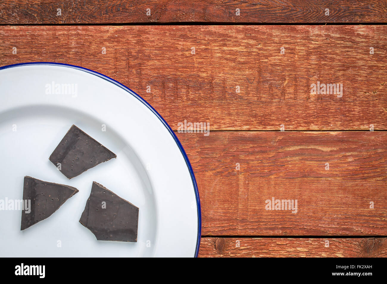 pieces of dark chocolate on white metal enamel plate against rustic ...
