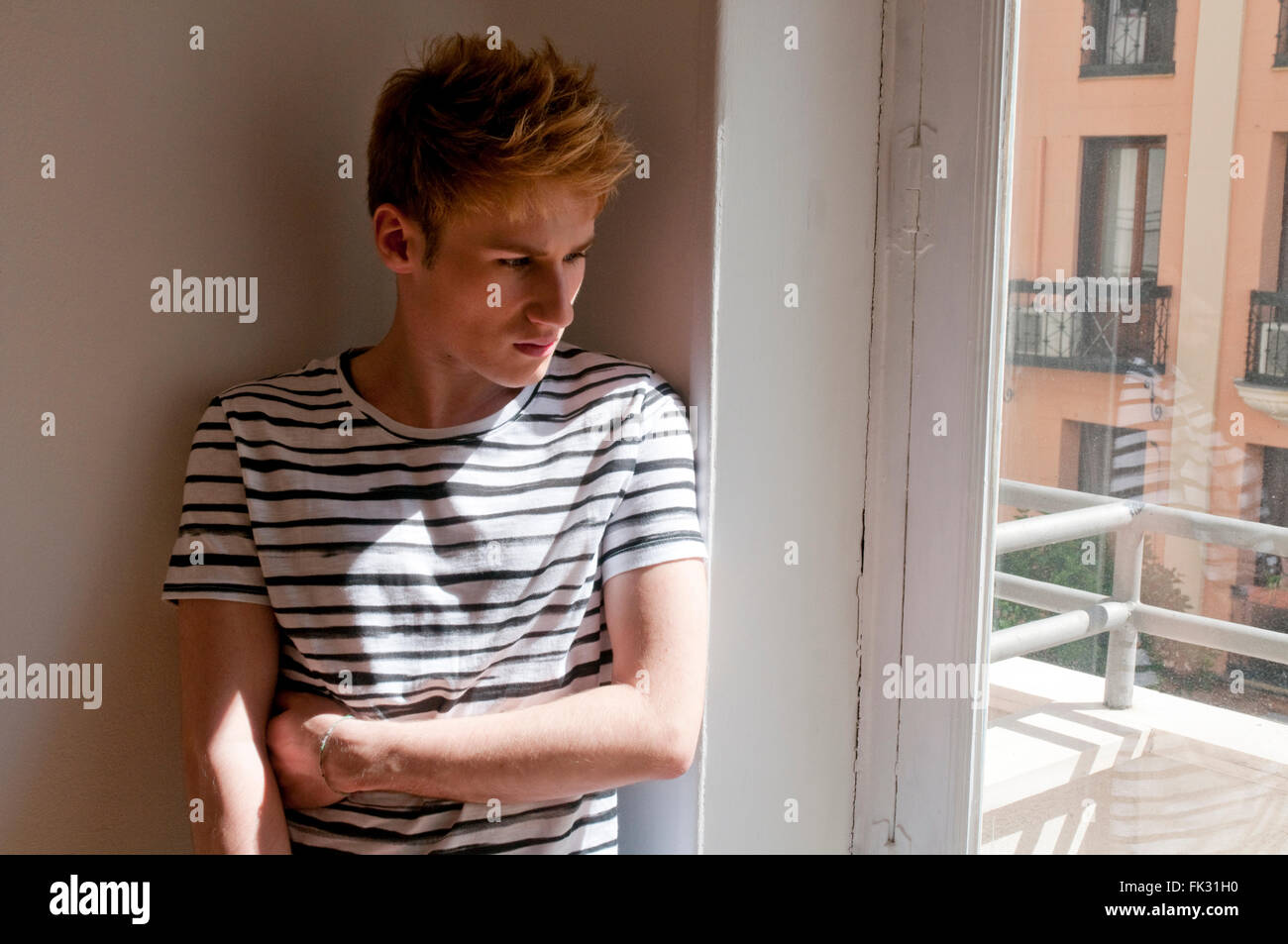 Young man by the window, leaned against the wall Stock Photo - Alamy