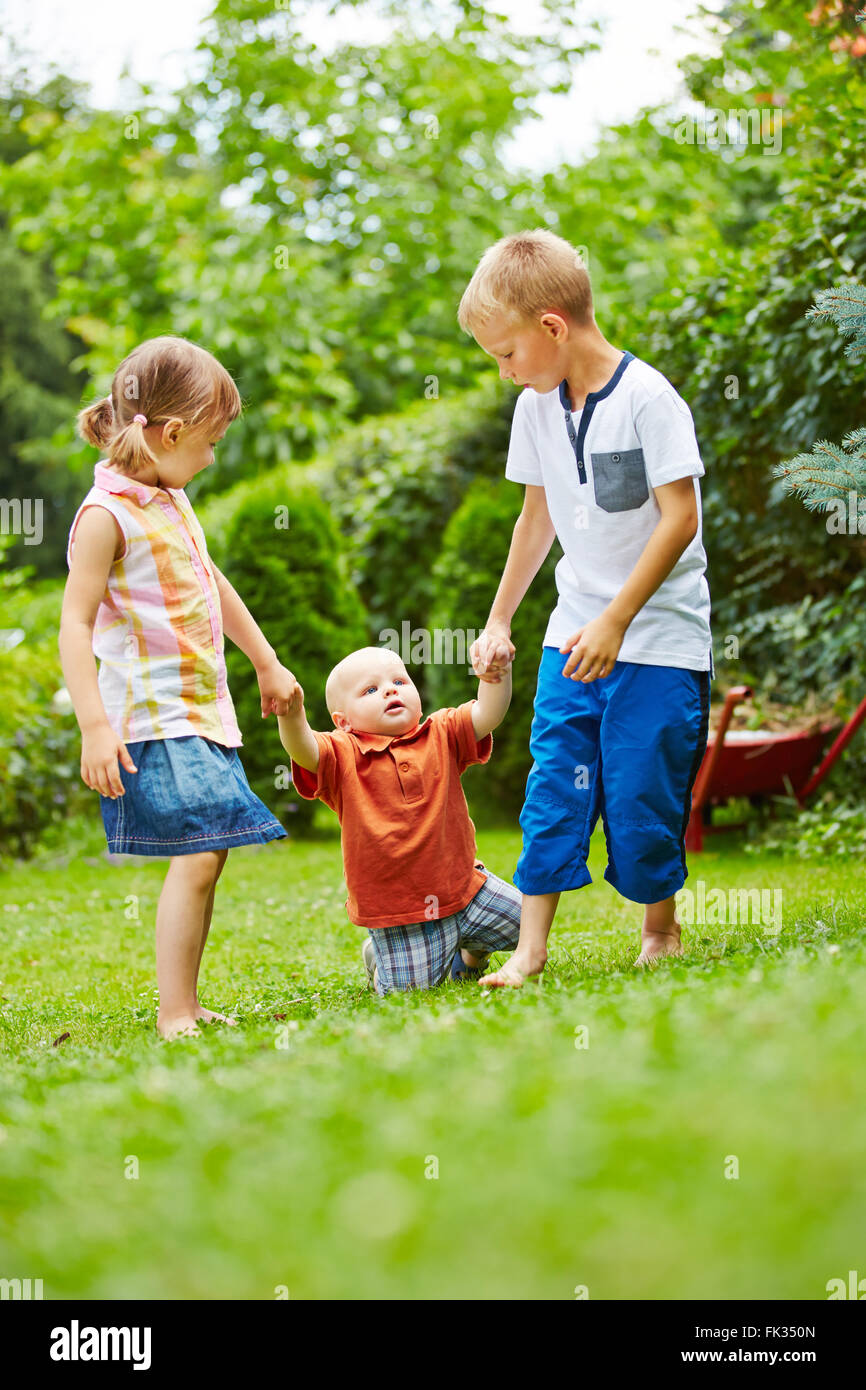 Two helpful children helping baby learning to walk in a garden in ...