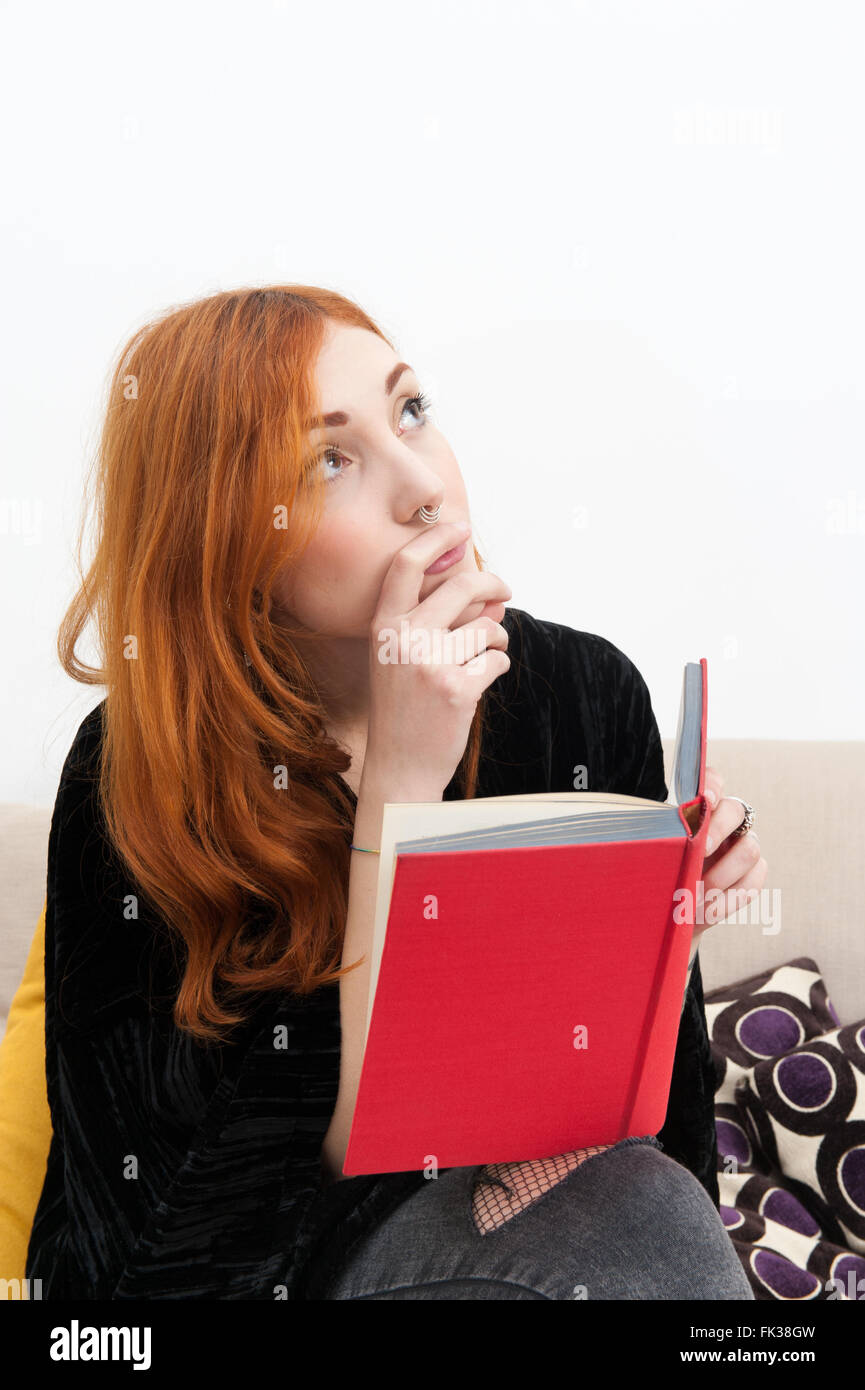 Young redhead woman reading a book with red empty cover looking up ...