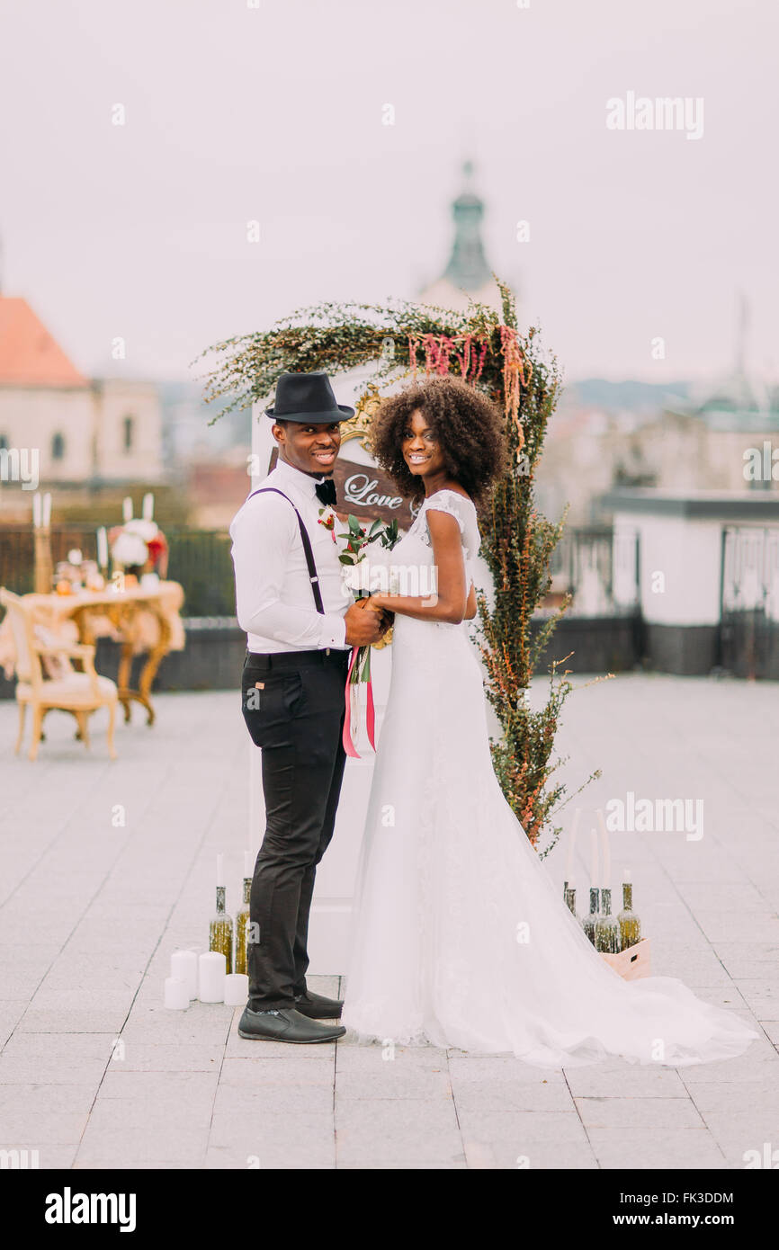 Happy african bride and groom posing for camera smiling on the rooftop ...
