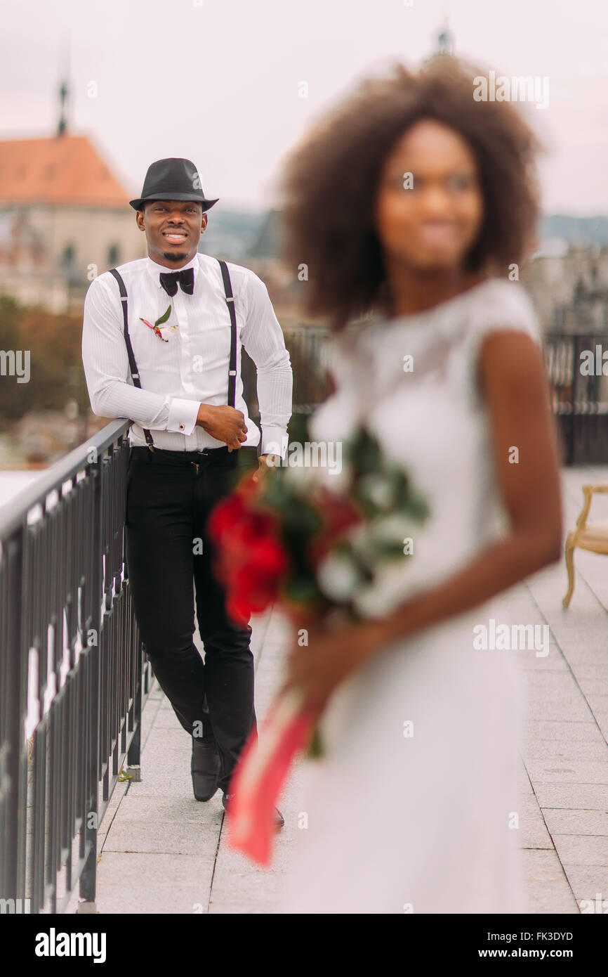 Stylish black groom in focus and his charming bride on the rooftop ...
