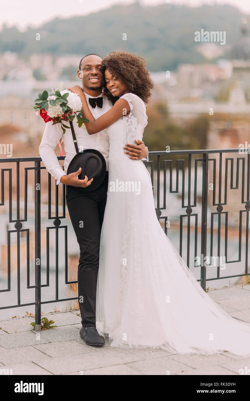 Happy black bride and groom softly hugging on the terrace with ...