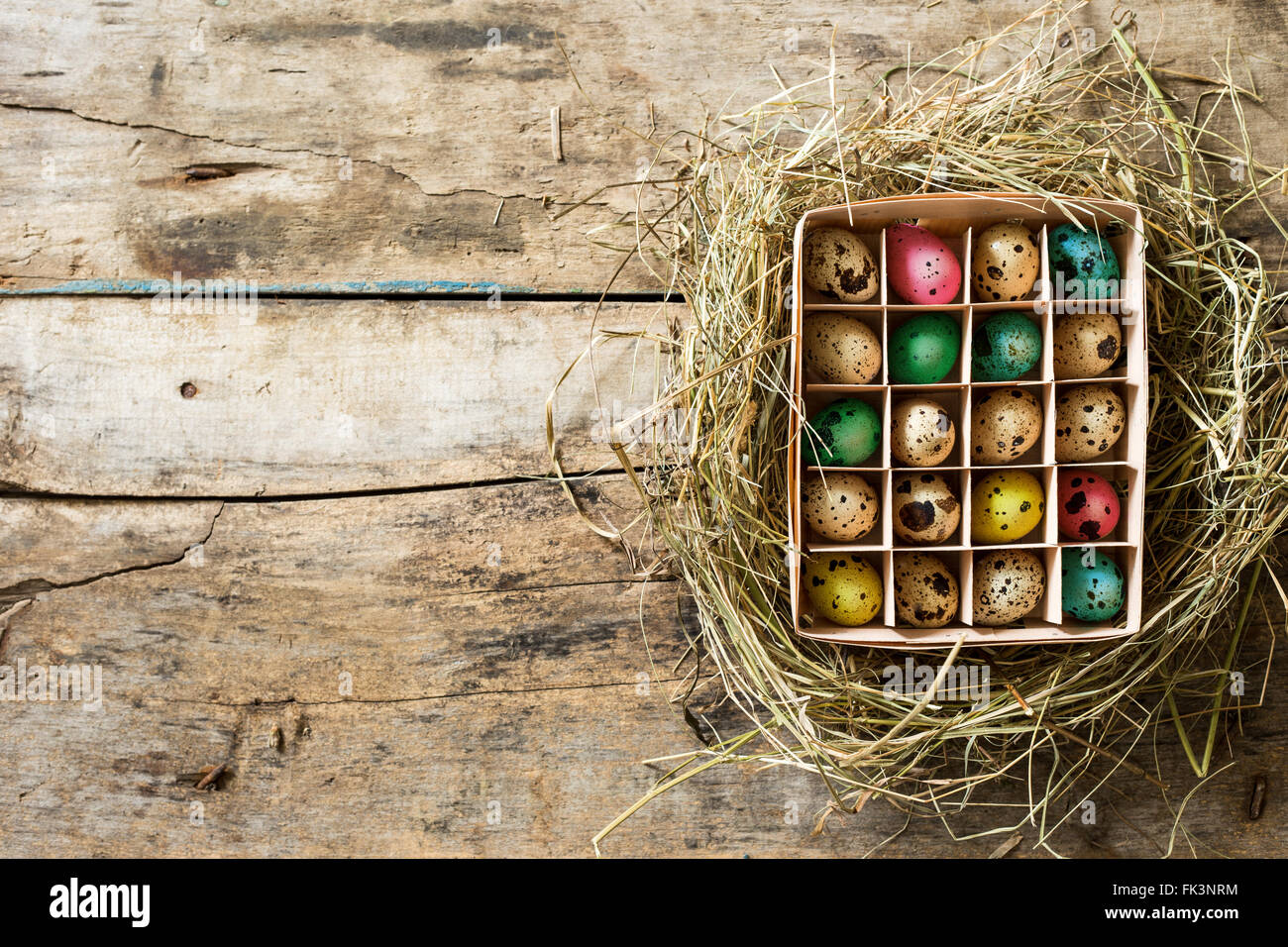 Easter wood background with box of colored eggs inside of hay nest ...
