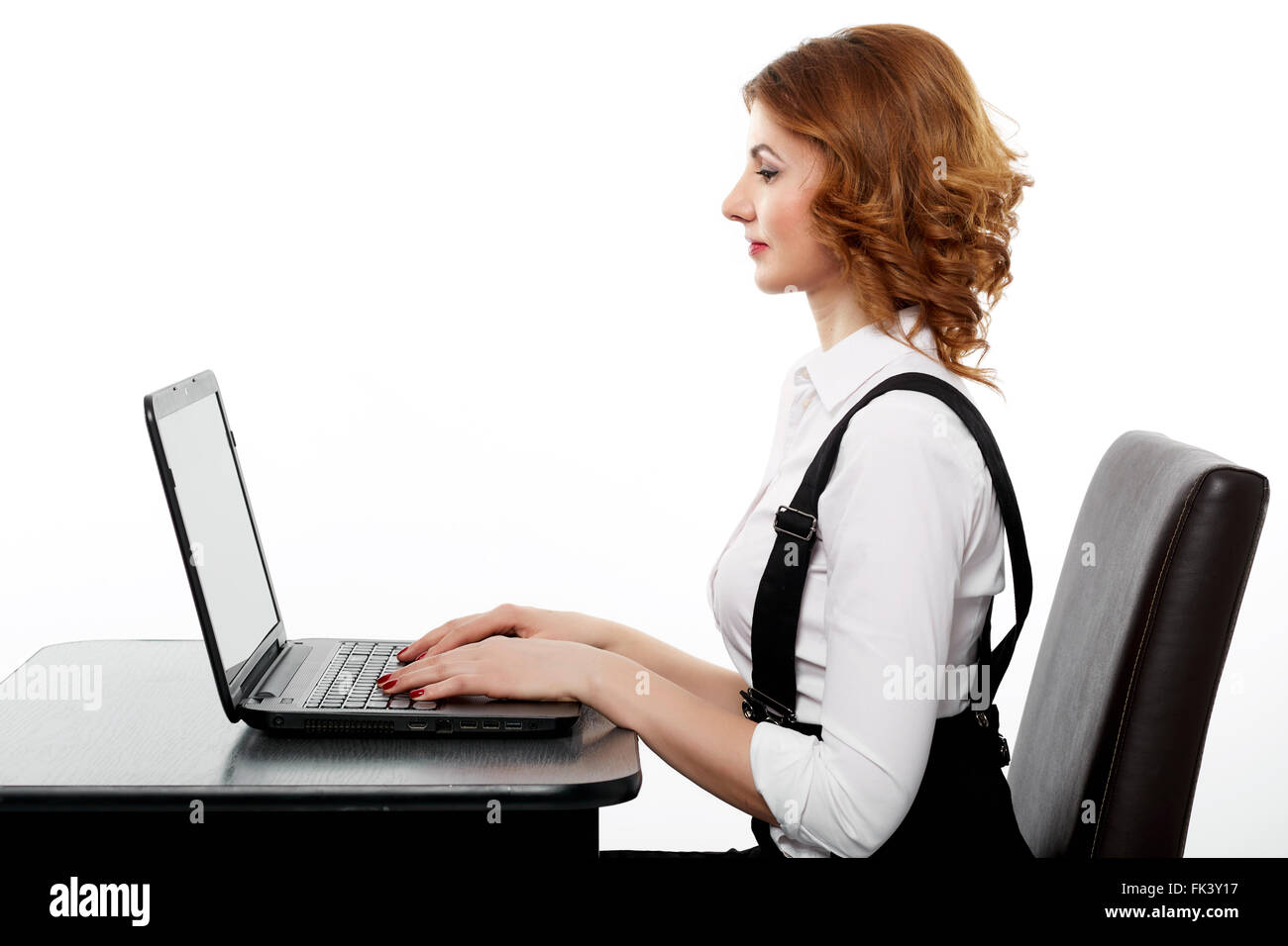 Profile of a pretty businesswoman sitting at her desk, using a laptop ...
