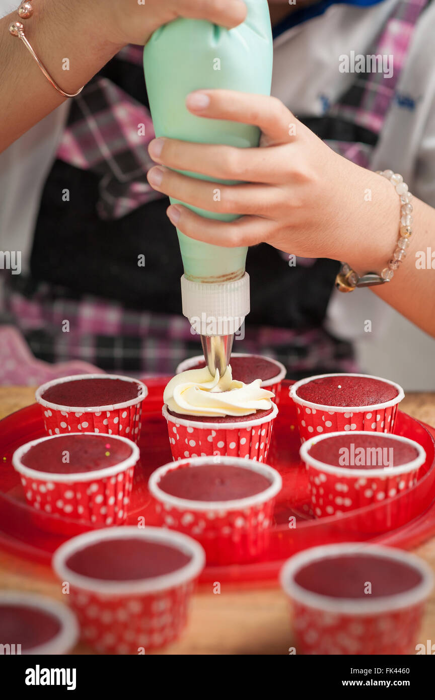 The action of making red velvet cupcakes. Woman hand piping cream ...