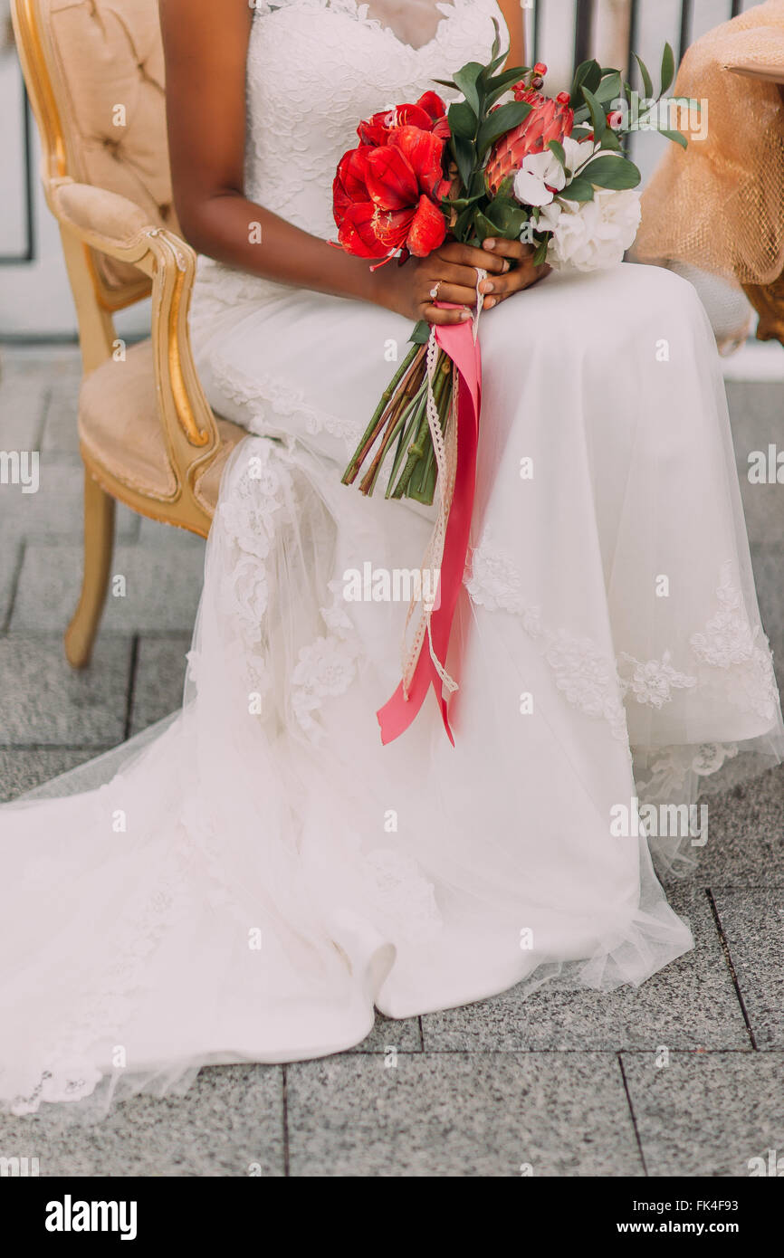 Beautiful african bride sitting on chair with bouquet of red flowes in ...