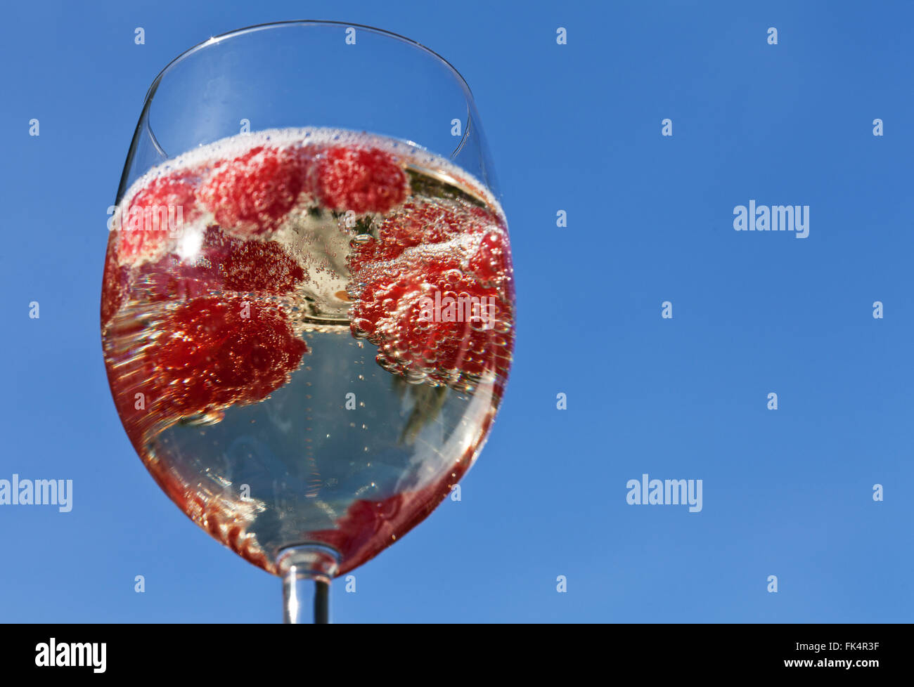 A glass of white wine, frozen strawberries and raspberries. Sunny blue ...