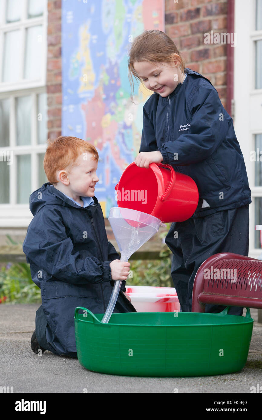 Two primary school pupils enjoying water play outside using various ...