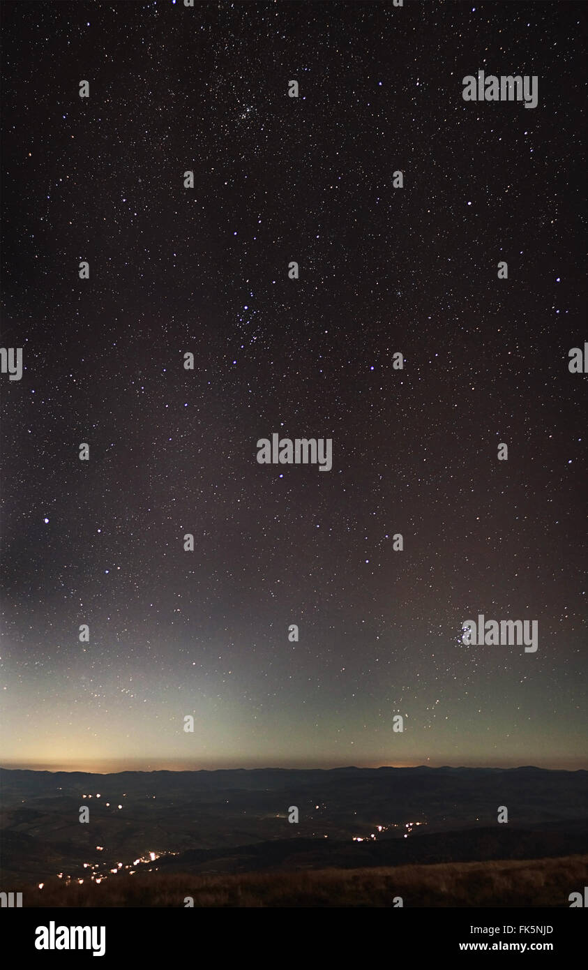 Stars over city lights and cloudy mountains panorama under moonlight ...