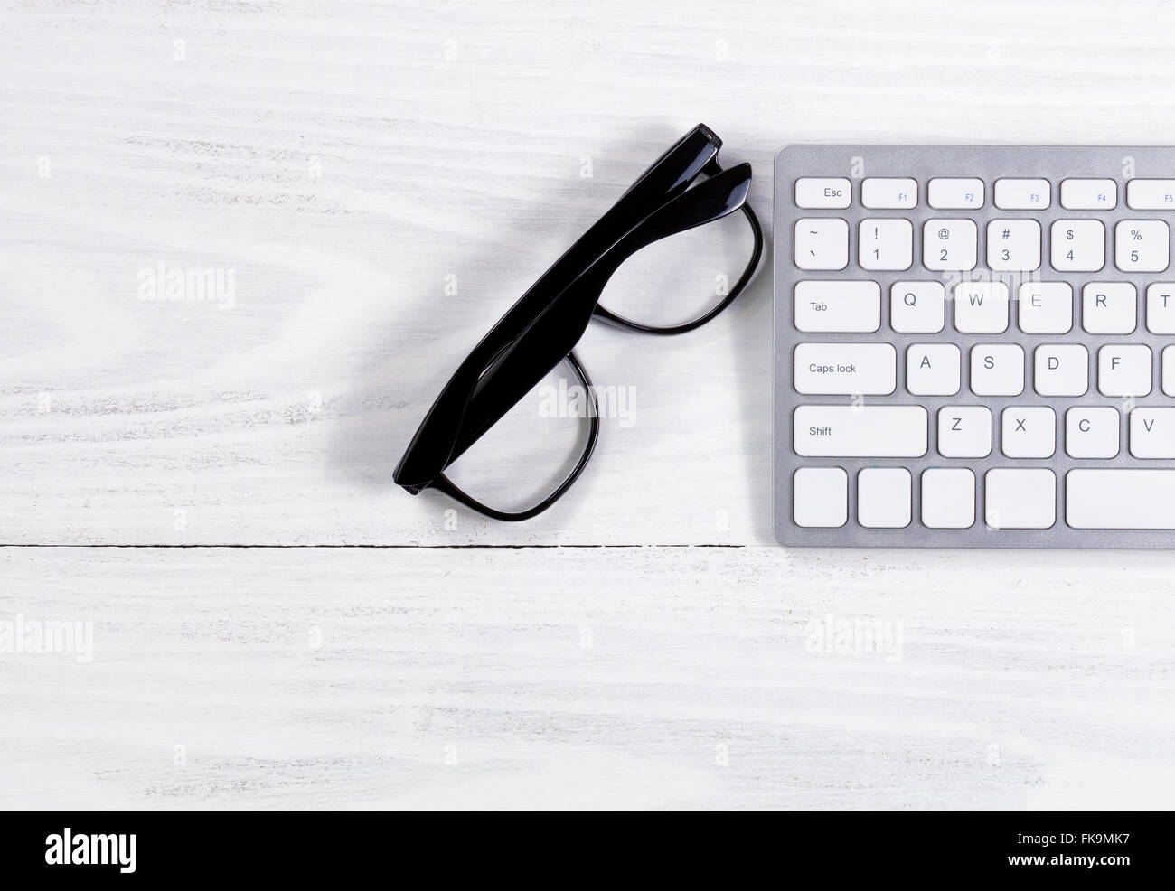 Overhead view of reading glasses and partial keyboard on white wood ...