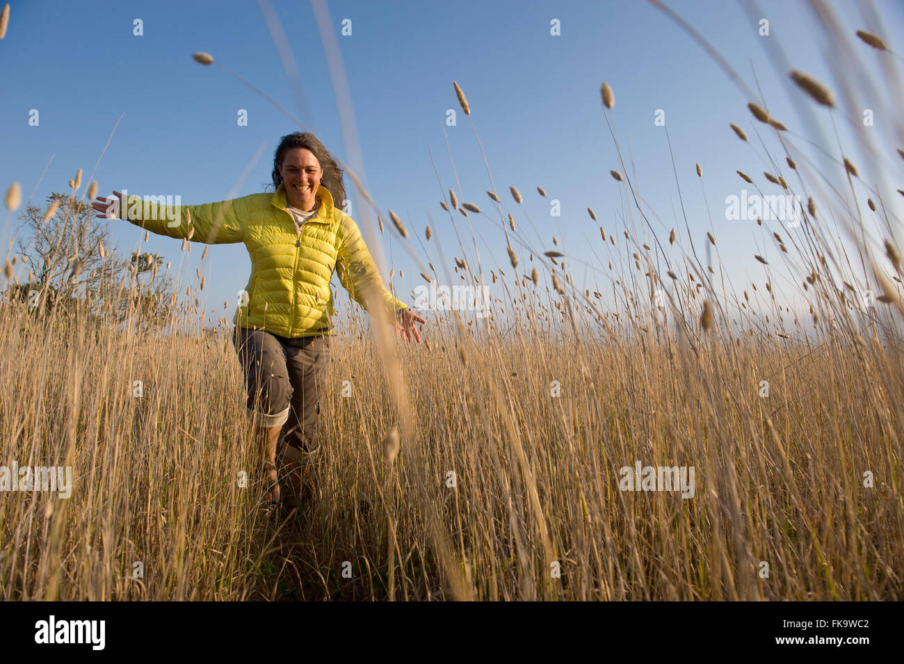Woman running through tall grass along the Pacific Coast in yellow ...