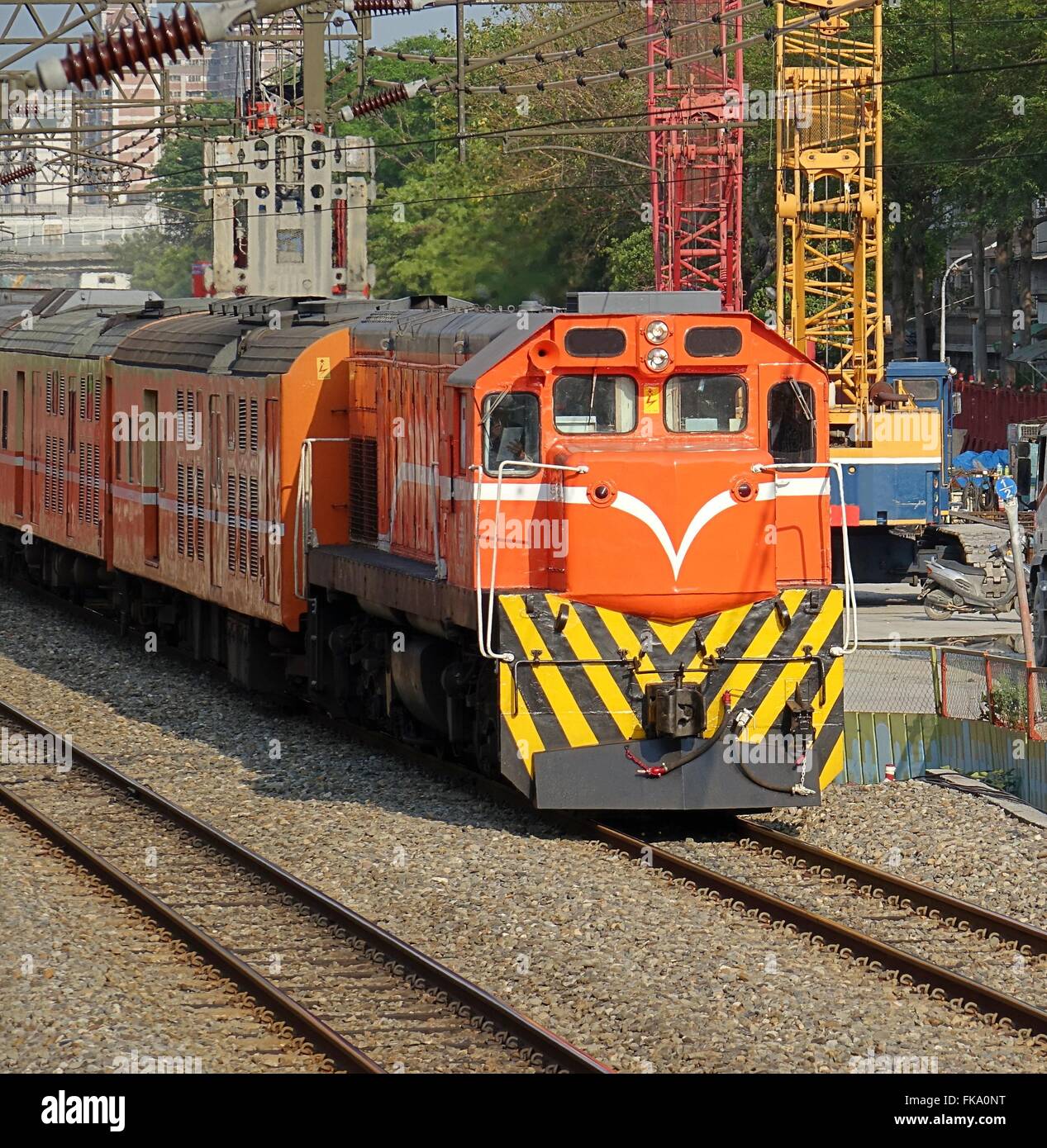 An orange colored diesel engine passes by a large scale construction ...