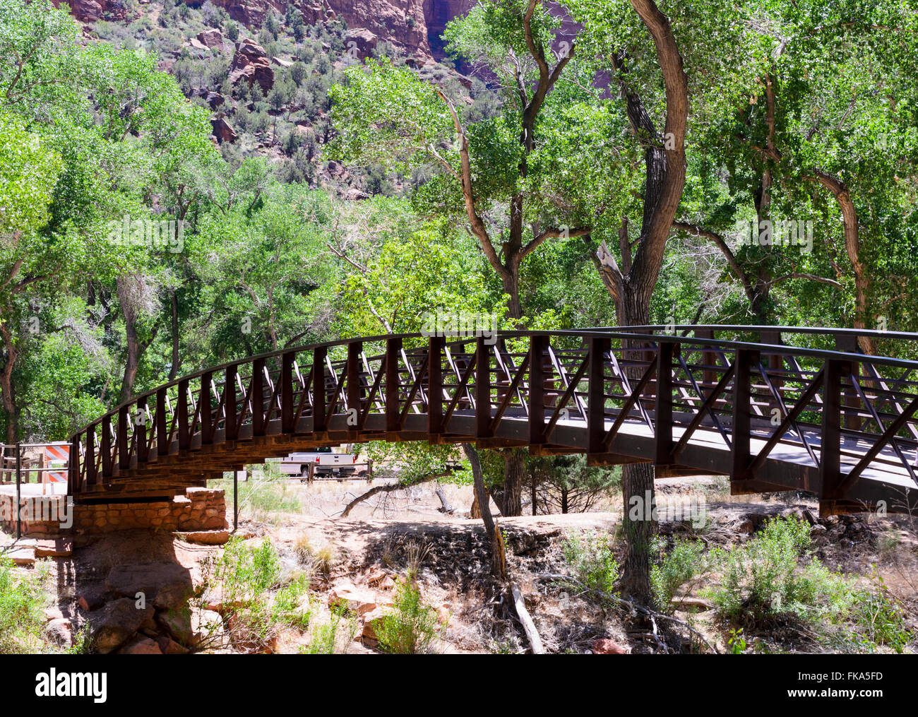 A walking bridge spans an unseen river below with green cotton wood ...