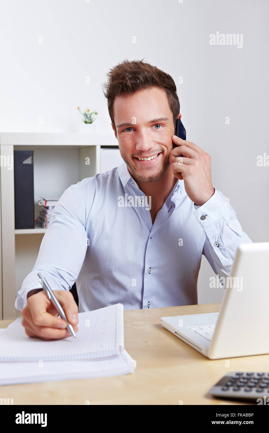 Happy business man in office making cell phone call and taking notes ...