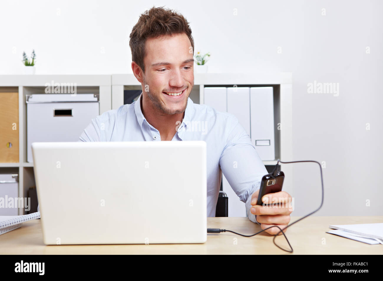 Young business man connection cell phone to computer in office Stock ...