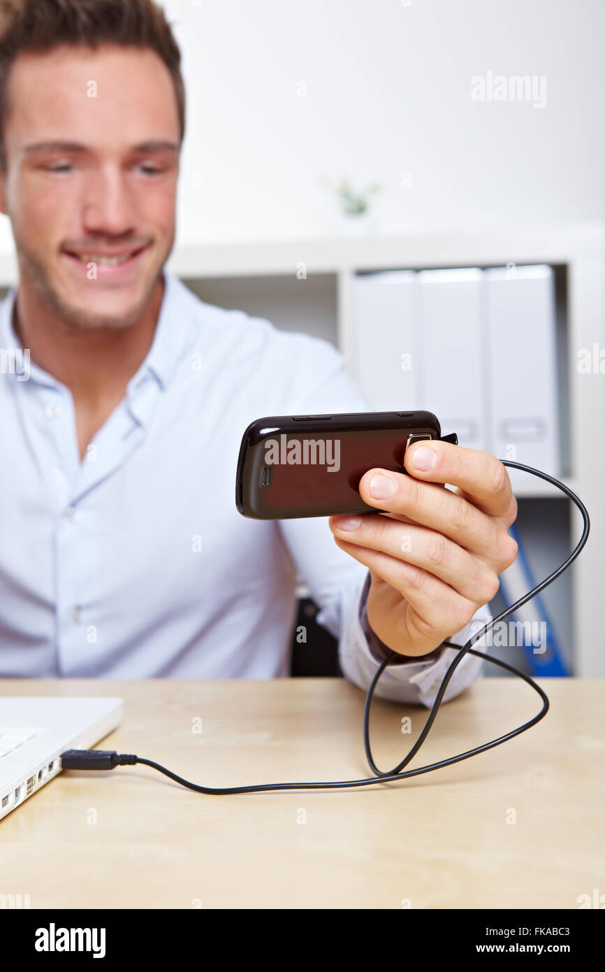 Young business man downloading images from cell phone to computer via ...