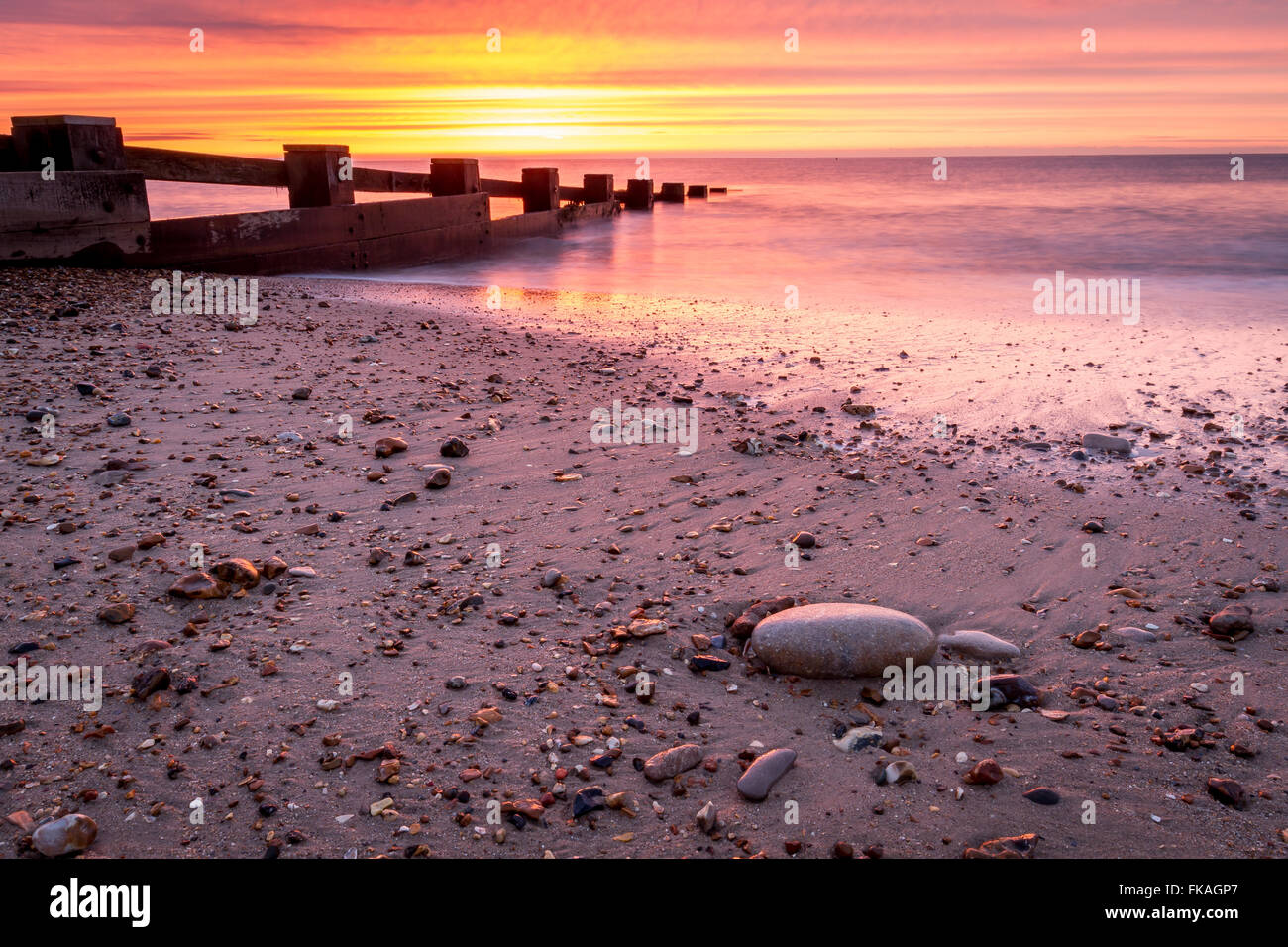 stones on sandy beach with groin at sunrise Stock Photo - Alamy