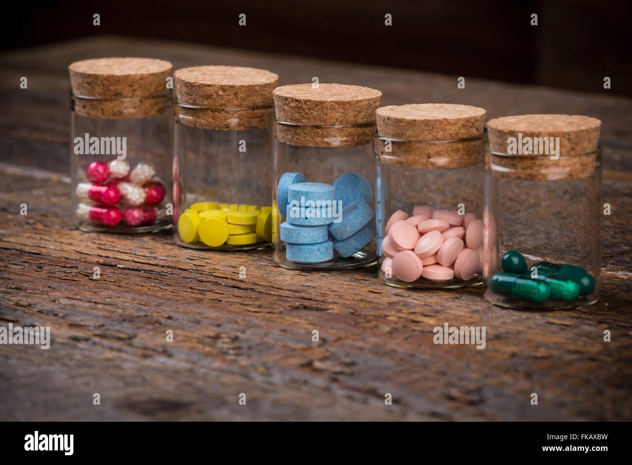 Various pills and capsules in glass containers with caps on dark wooden ...