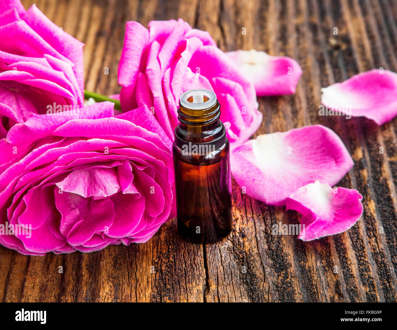 Rose essential oil in a bottle with pink roses and petals on wooden ...