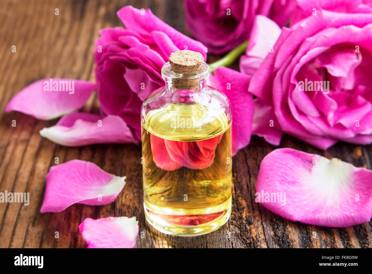Rose essential oil in a bottle with pink roses and petals on wooden ...