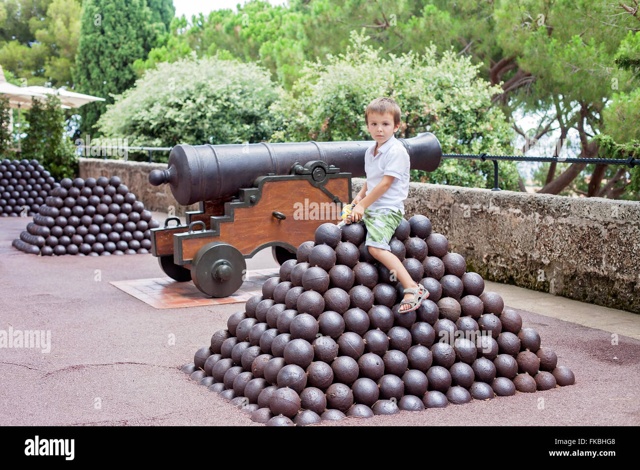 Preschool boy, sitting on a pile of cannon-balls in the village of ...
