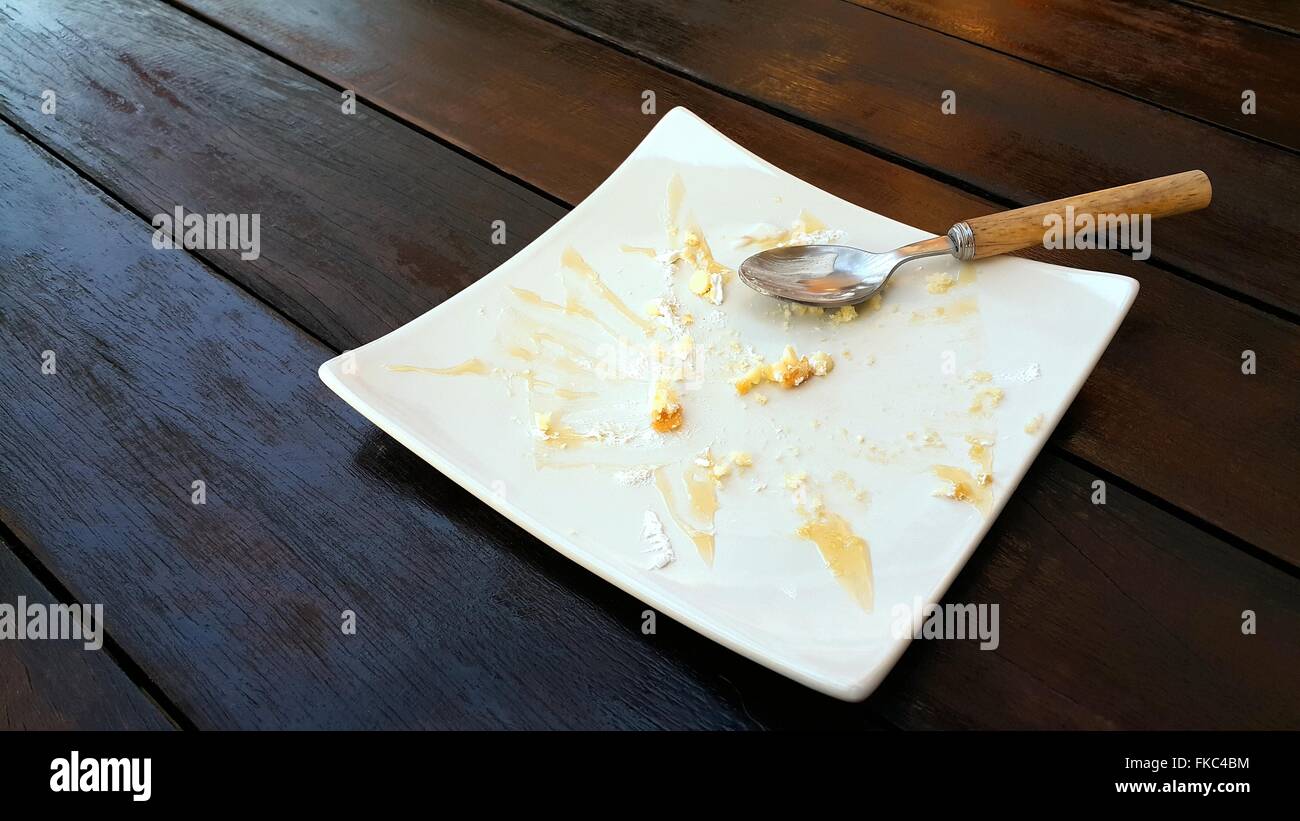 Empty Plate with crumbles of eaten cake and used spoon on wooden table ...