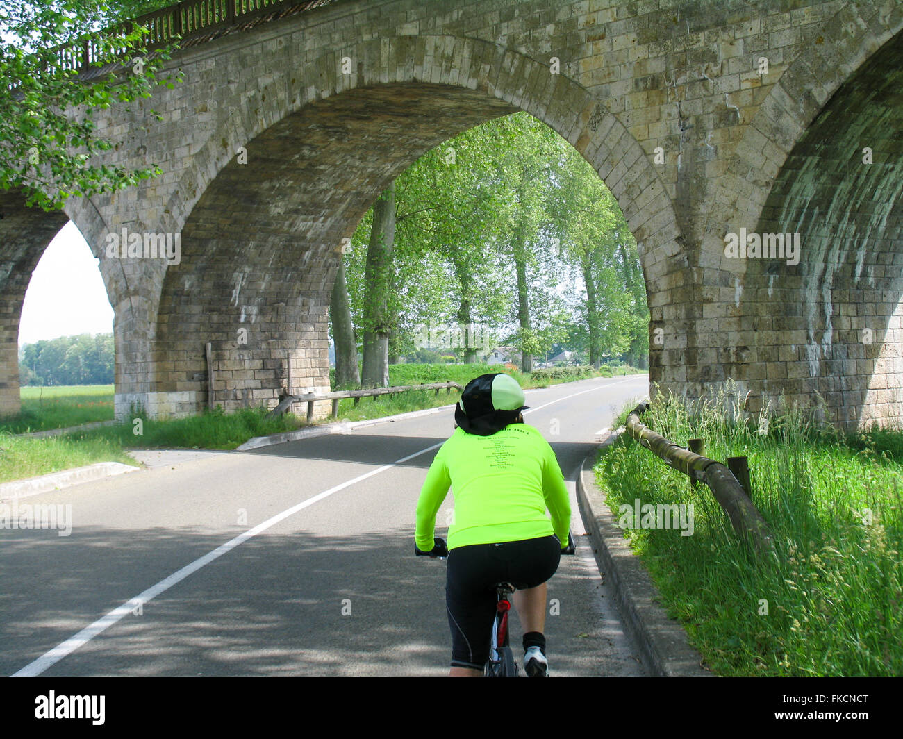 A female touring cyclist riding her bike on a road passing under a ...