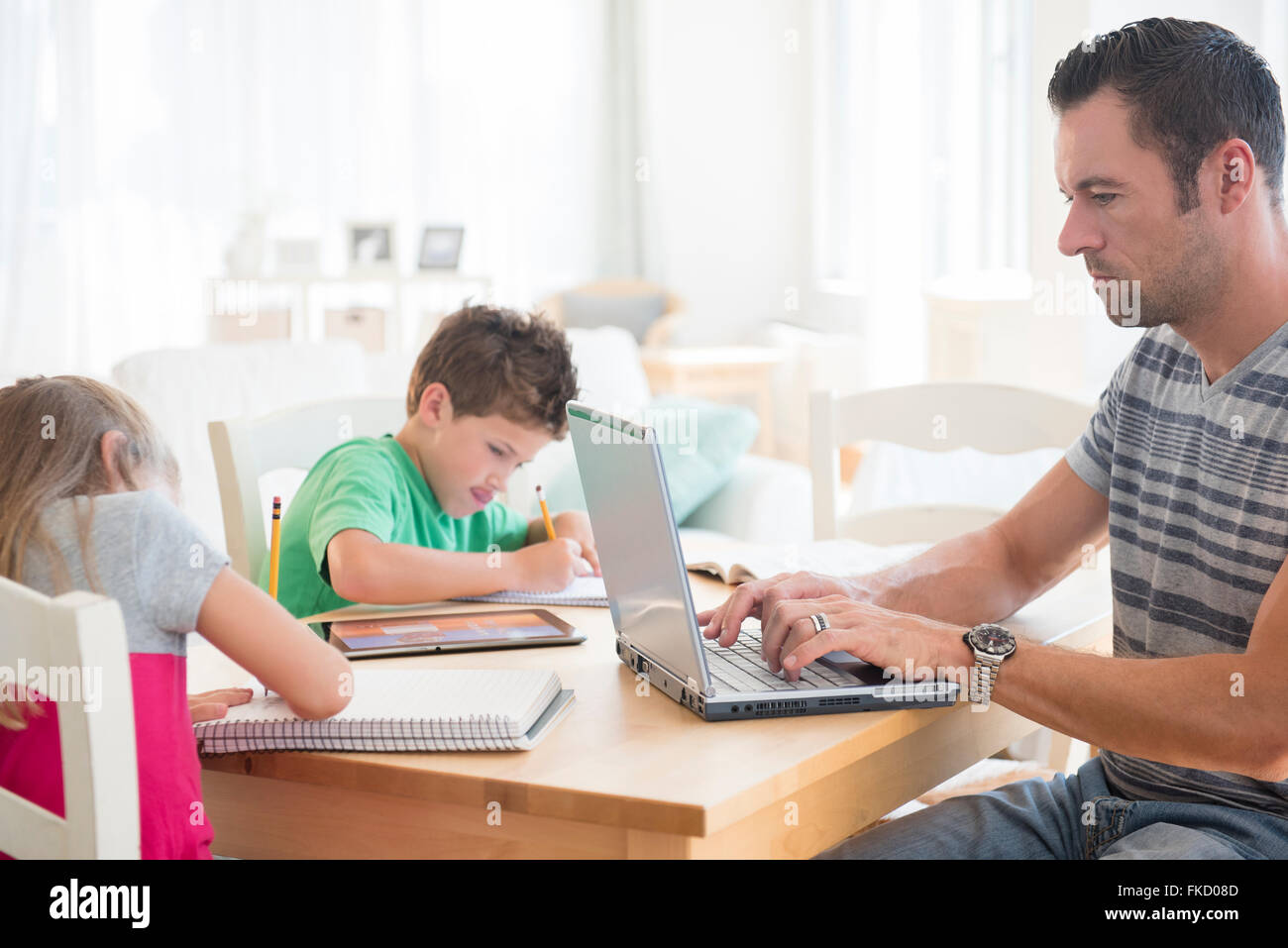 Man using laptop with two children (6-7, 8-9) writing in notepads Stock ...