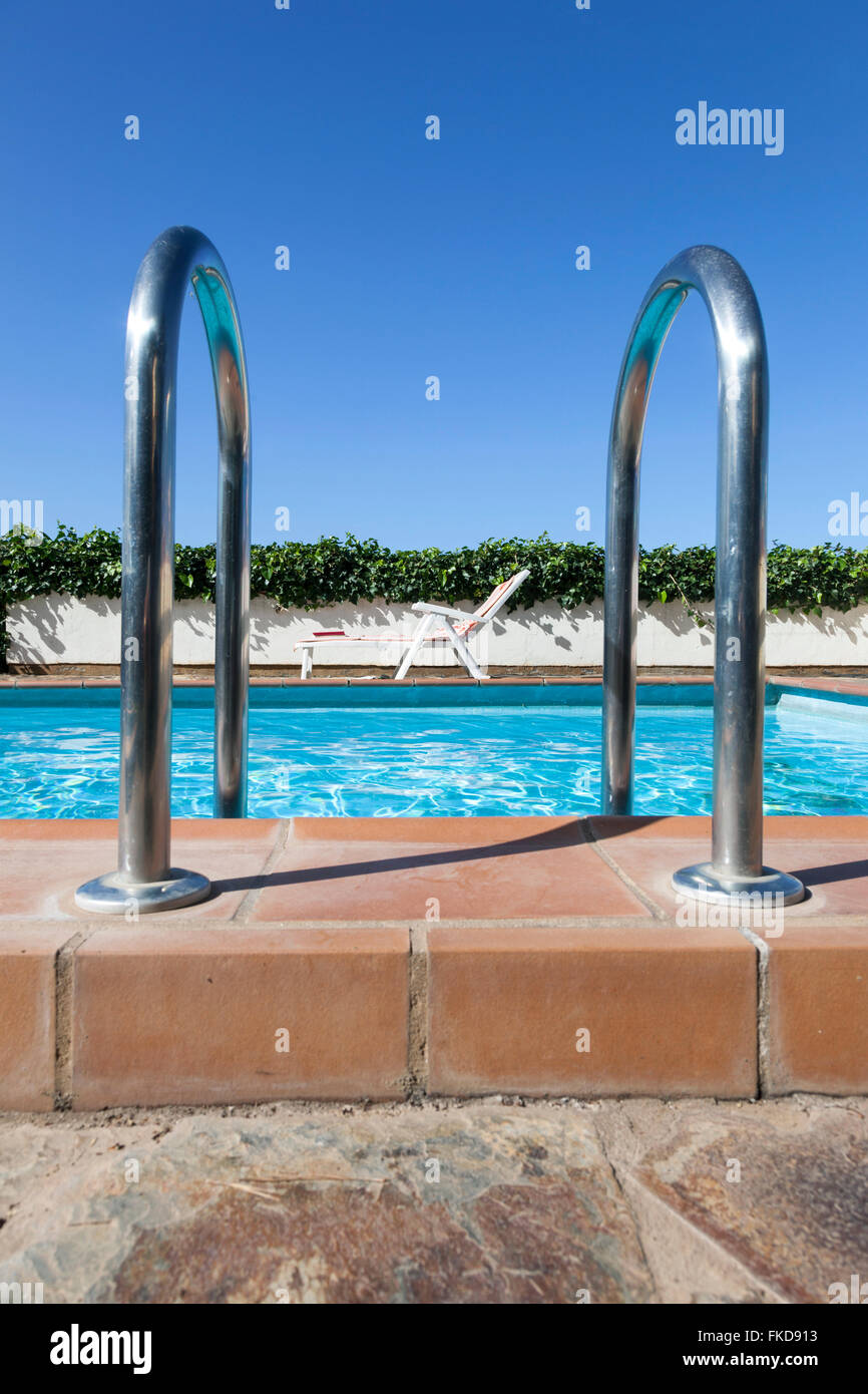 entrance to swimming pool with ivy on wall and blue sky and deck chair ...