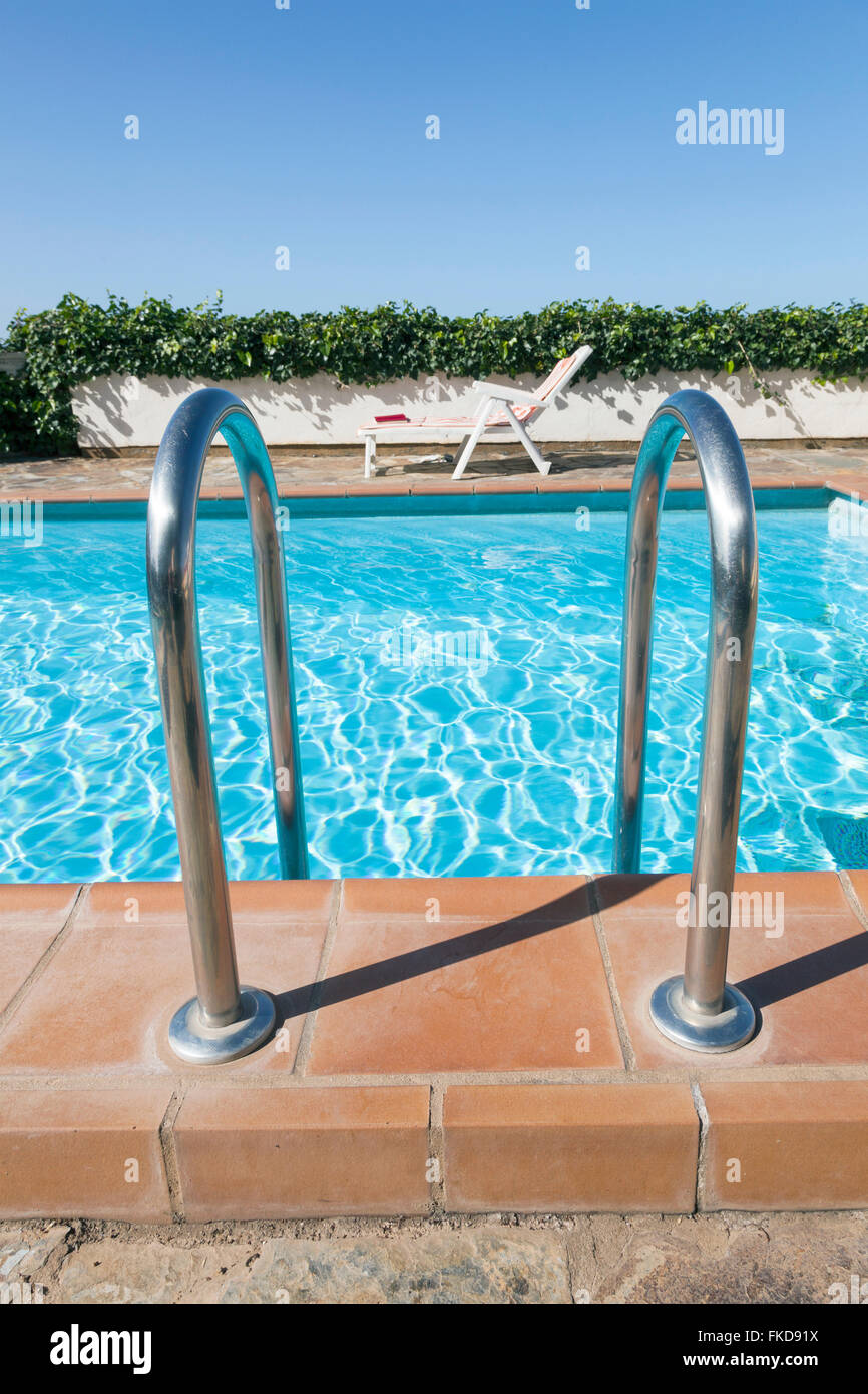 entrance to swimming pool with ivy on wall and blue sky and deck chair ...
