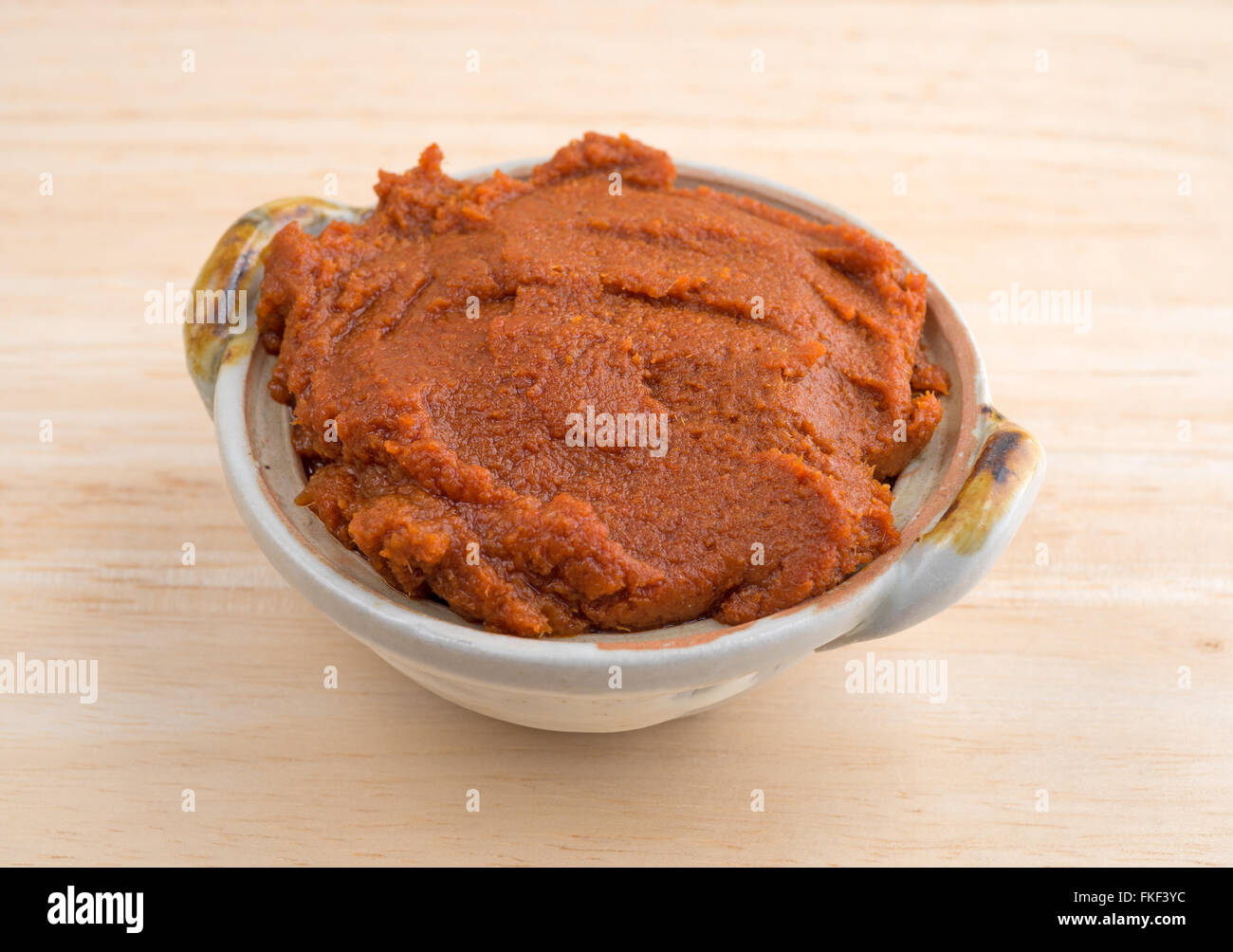 Side view of a small bowl filled with red curry paste on a wood table ...