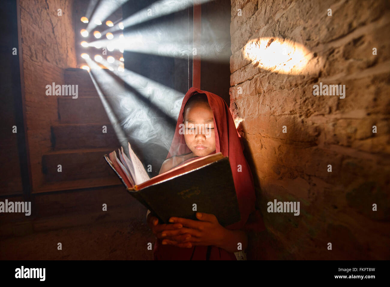 A young monk reading with rays of sunlight in the temples of Bagan ...
