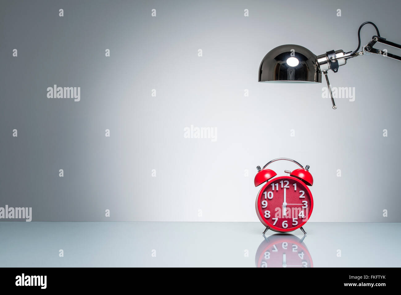 lighting up red alarm clock with desk lamp on round studio lighting ...