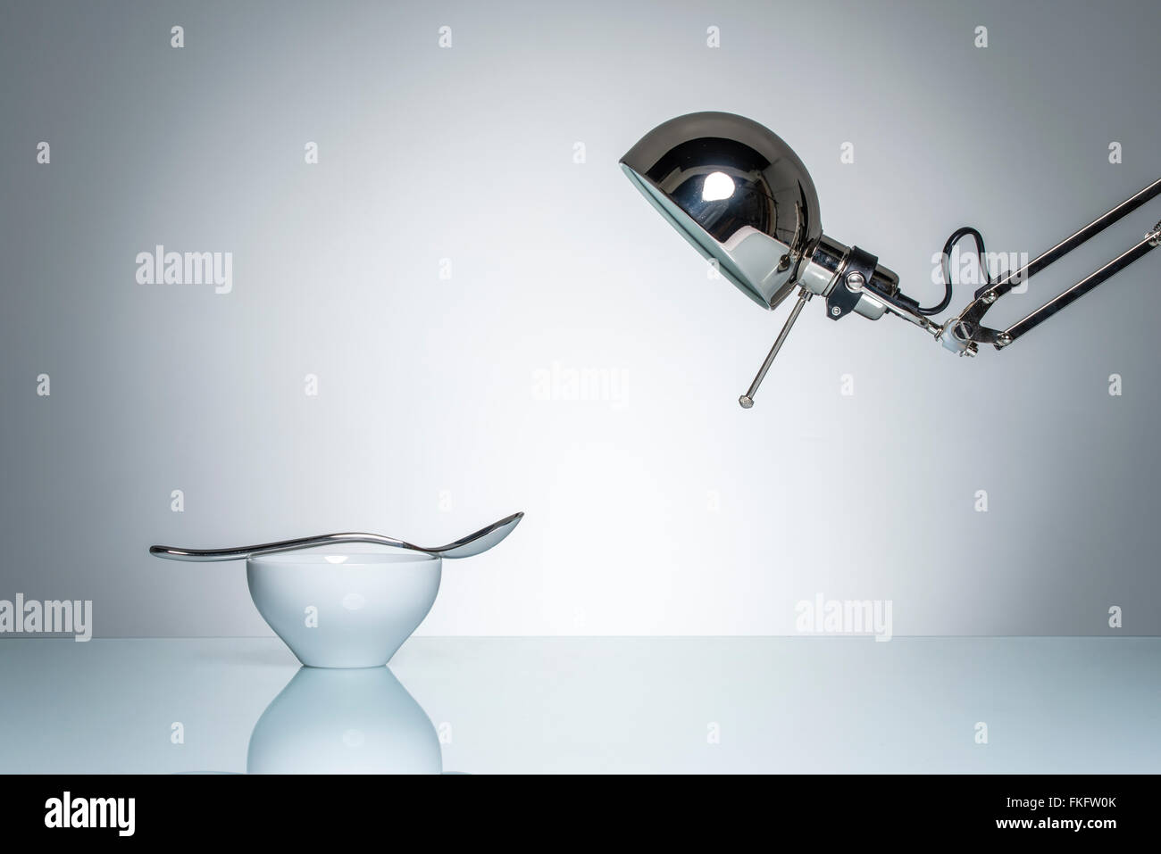 lighting up white ceramic bowl silver spoon with desk lamp on round ...