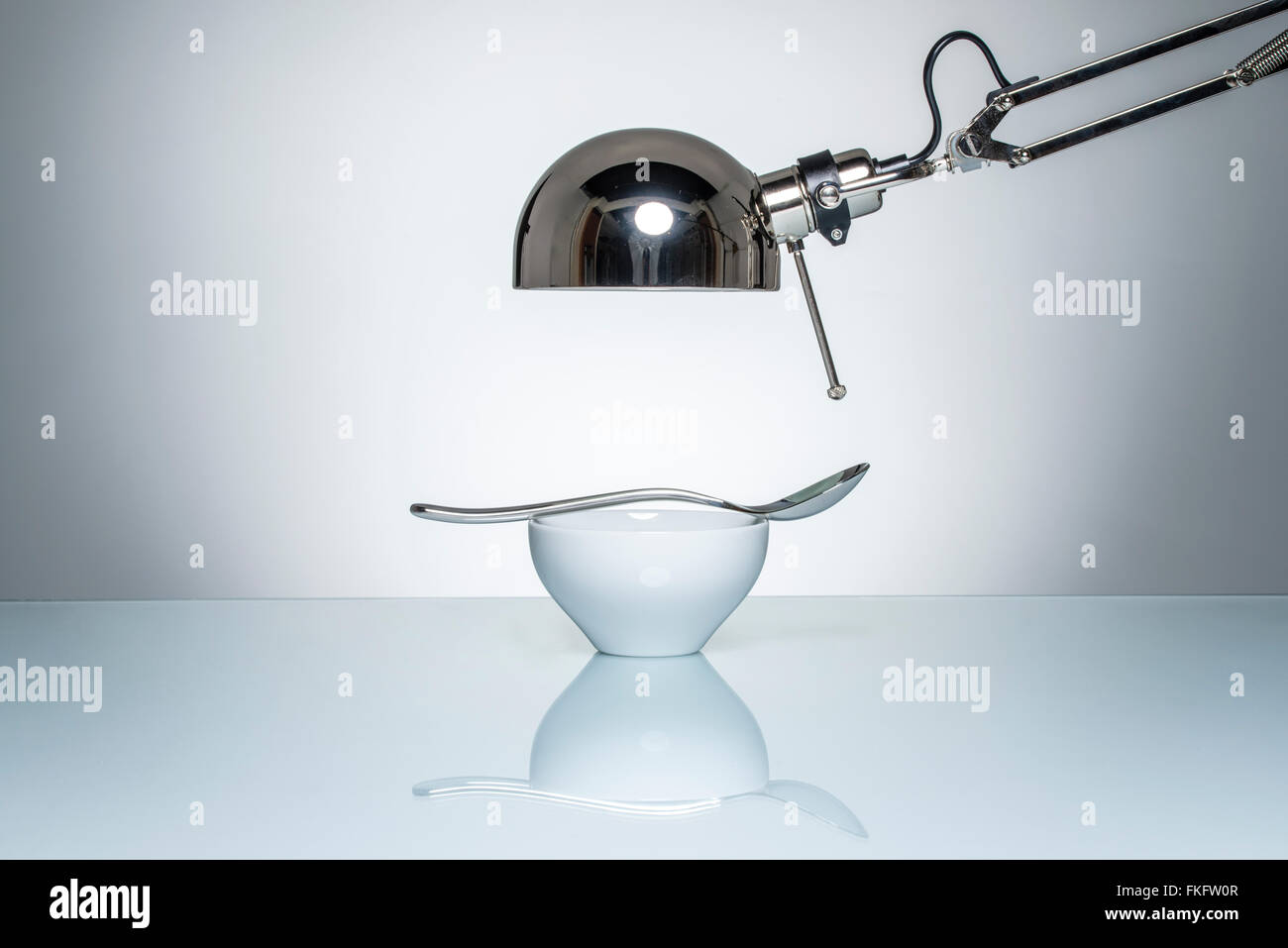 lighting up white ceramic bowl silver spoon with desk lamp on round ...