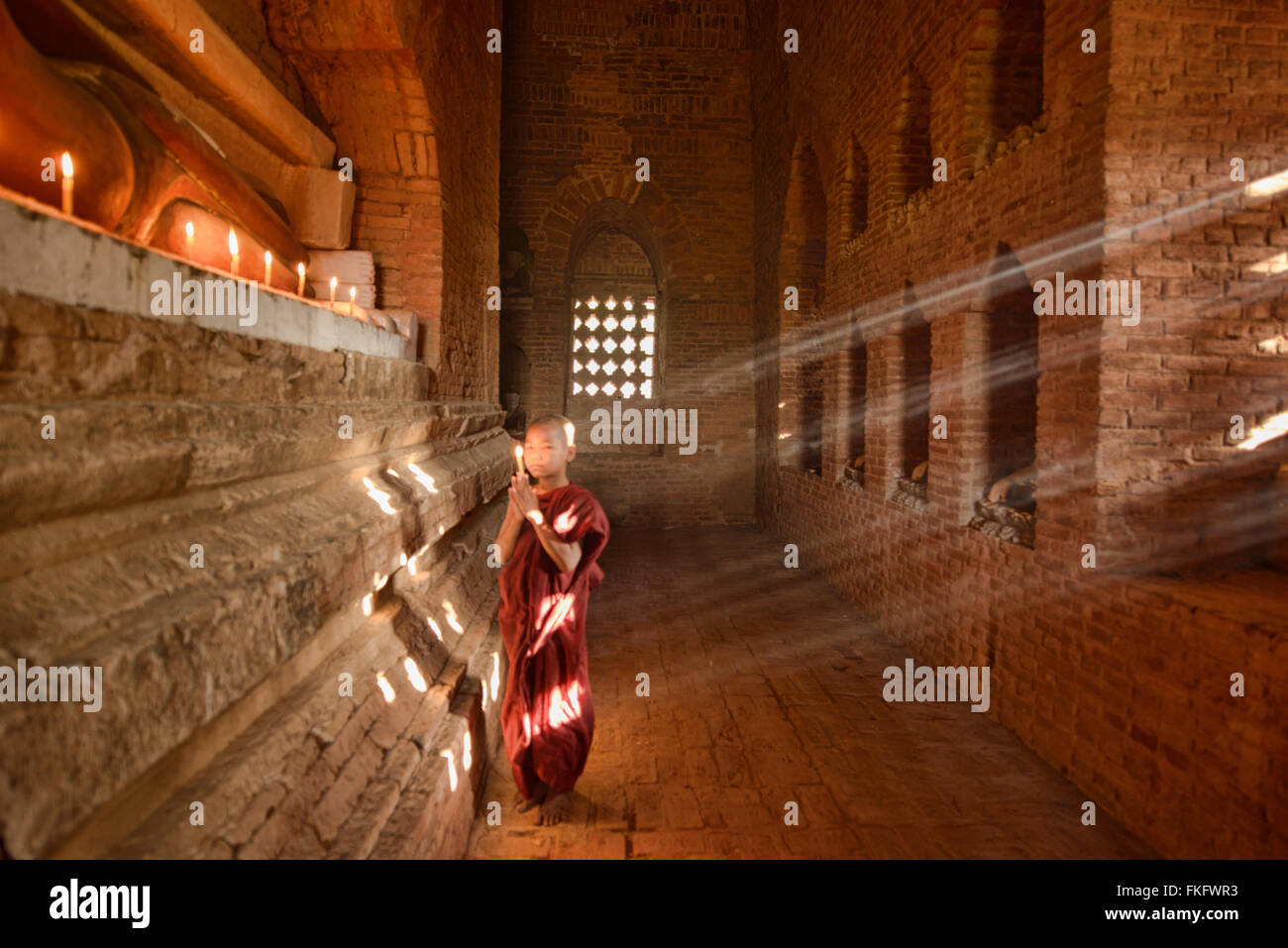 A young monk praying with rays of sunlight in the temples of Bagan ...
