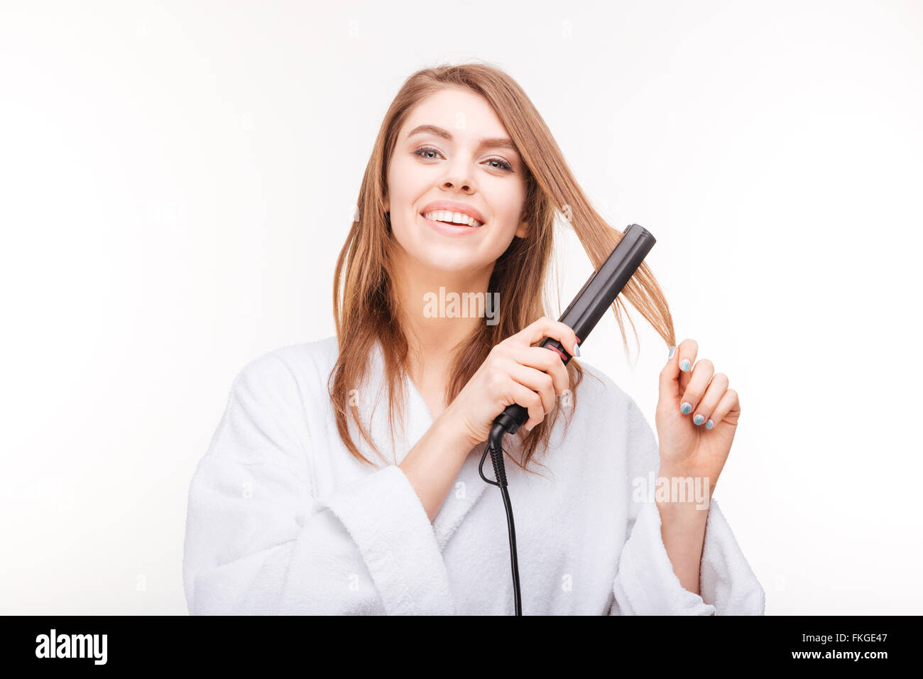 Cheerful attractive young woman straightening her hair with hair ...