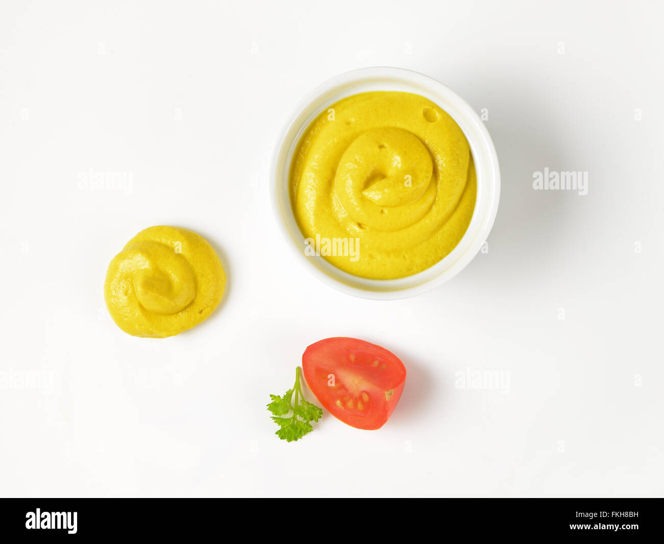 bowl and swirl of yellow mustard and slice of tomato on white ...