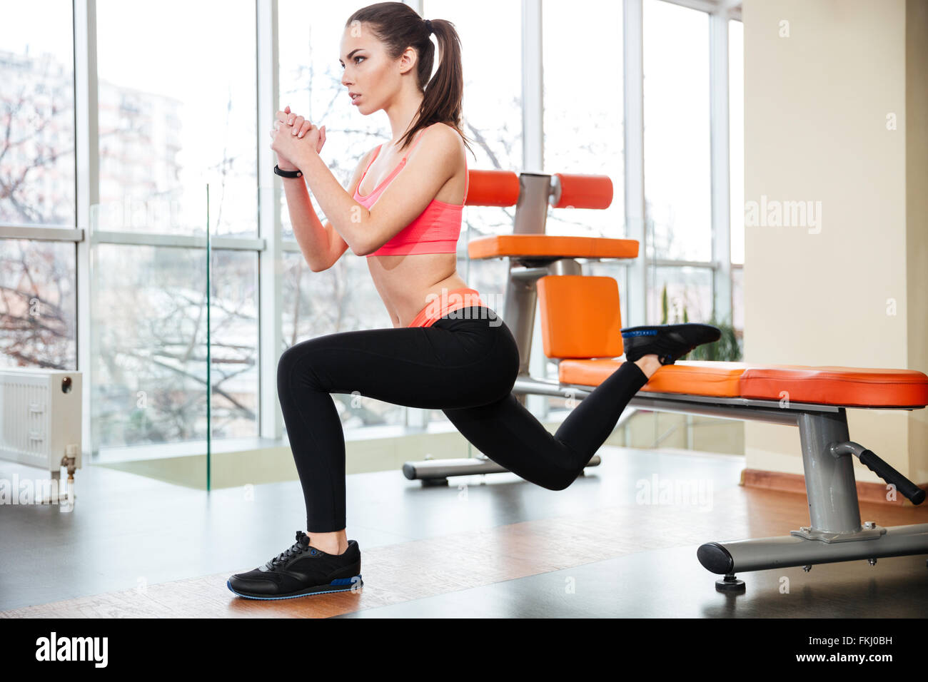 Pretty concentrated young sportswoman doing squats using bench in gym ...