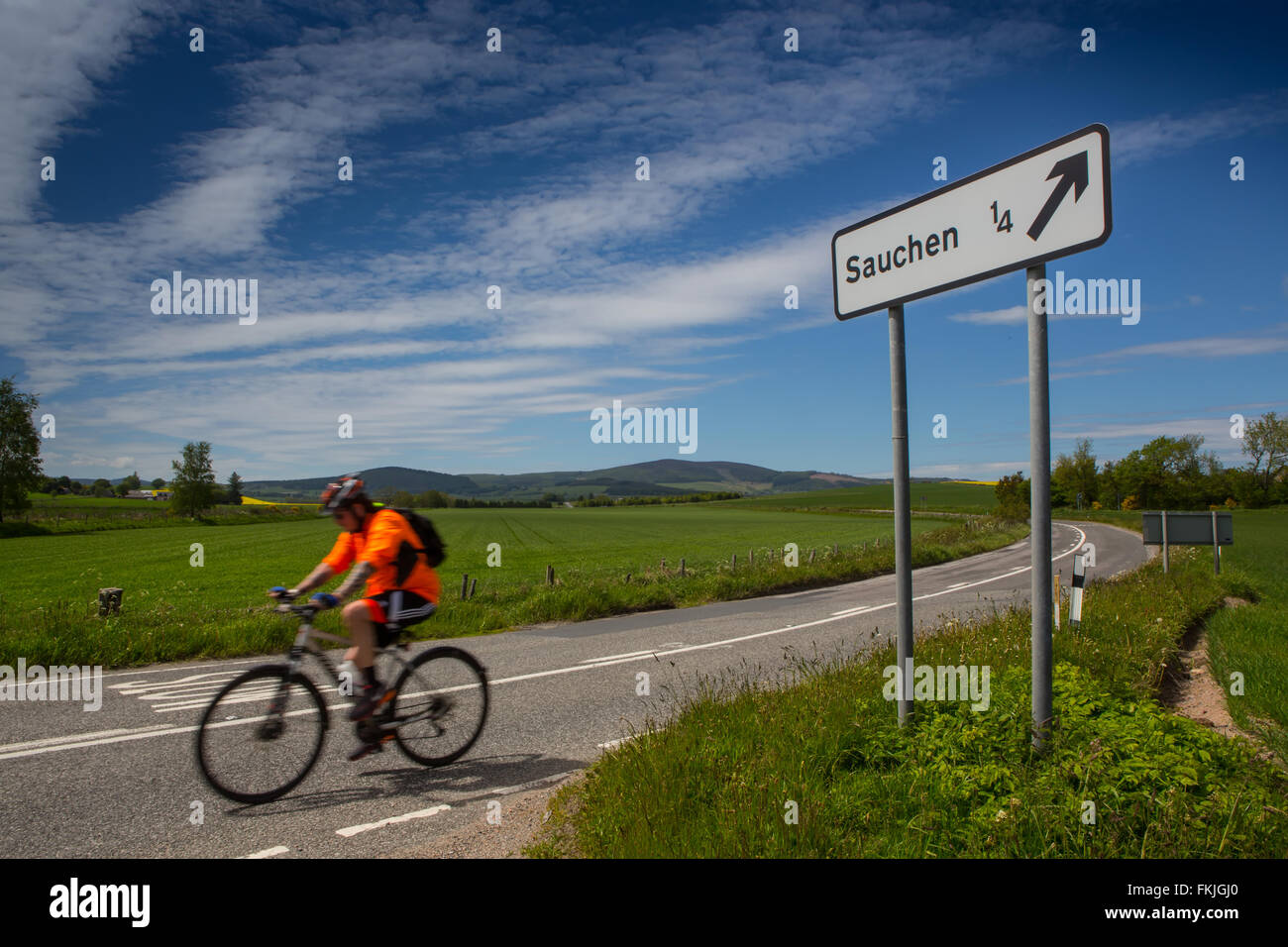 A cyclist riding past the sign for the village of Sauchen in ...