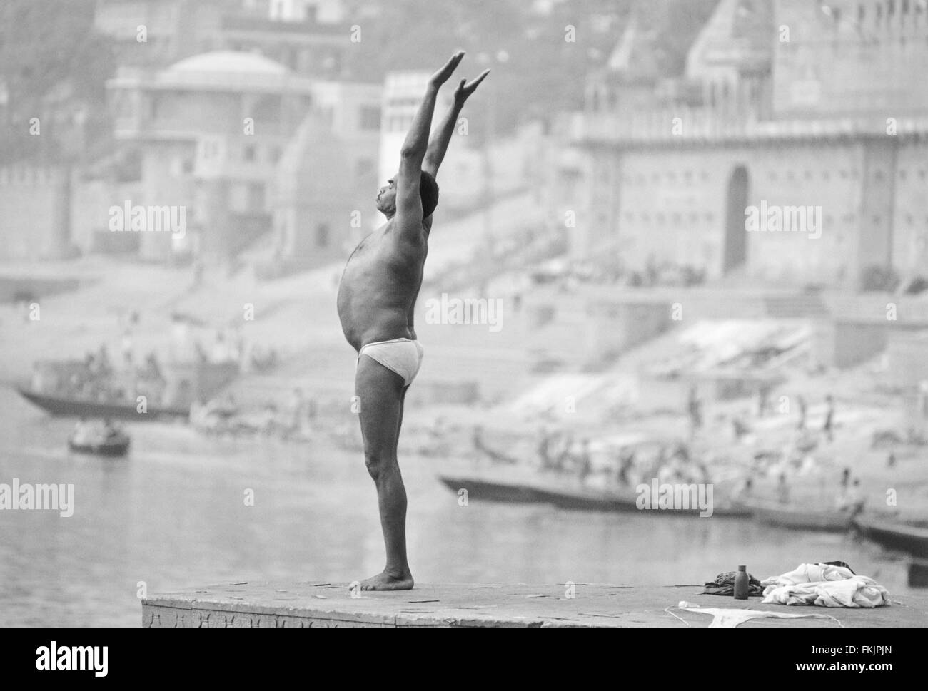 At sunrise man doing yoga postures,poses,routine facing rising sun.On ...