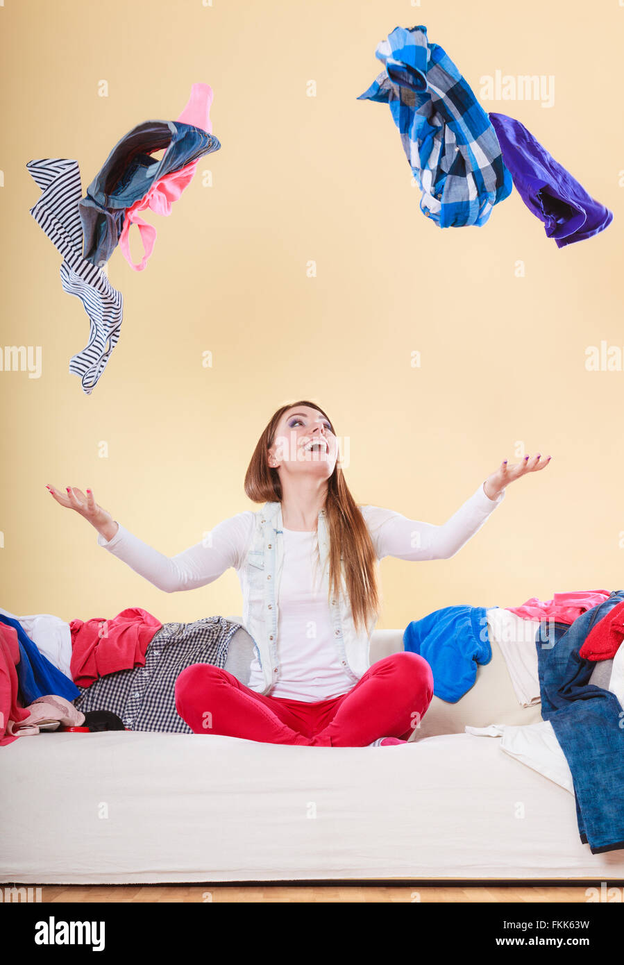 Happy woman sitting on sofa couch in messy living room throwing clothes ...