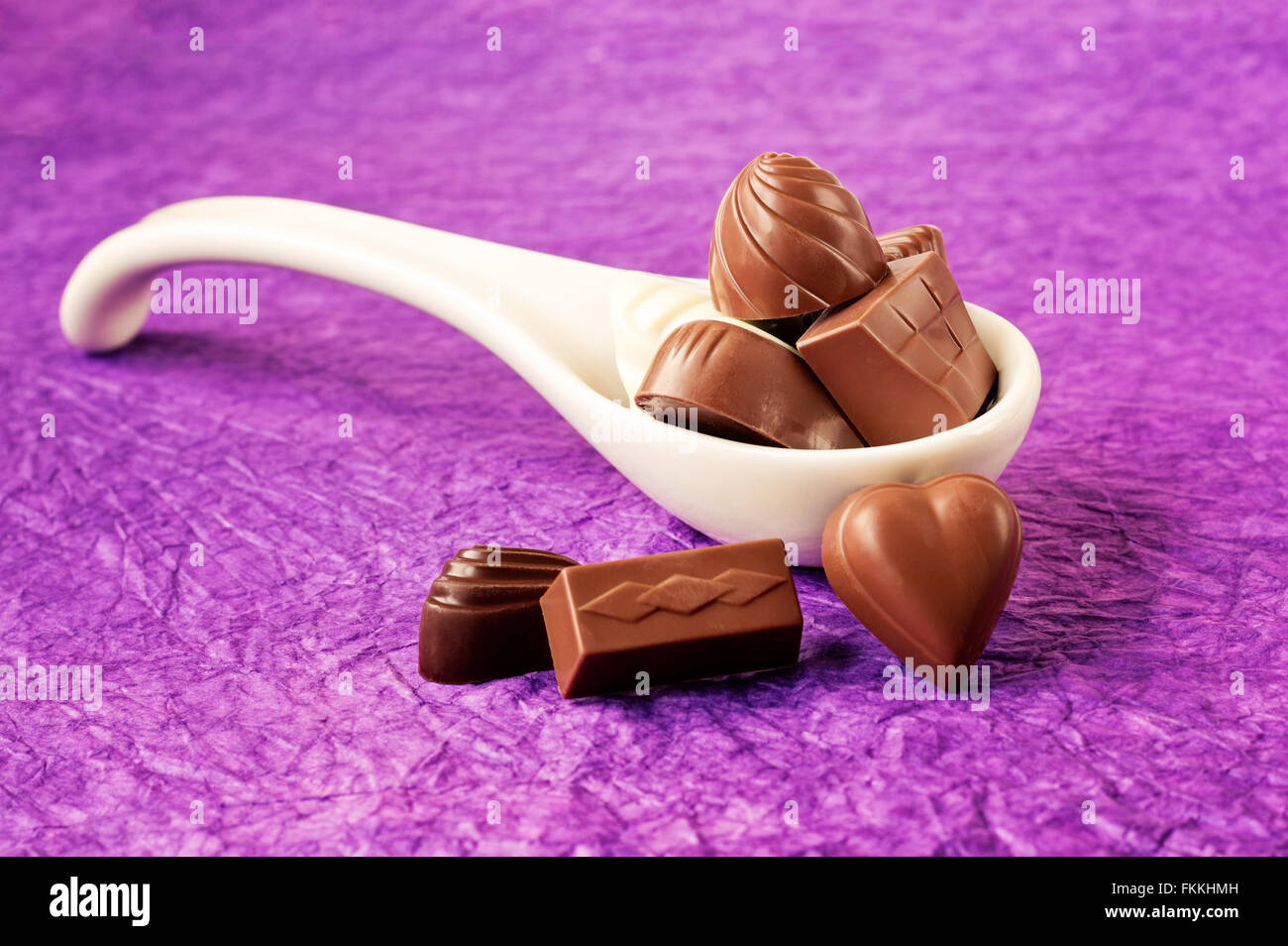 White, dark and milk chocolate pralines in a ceramic spoon on a purple ...