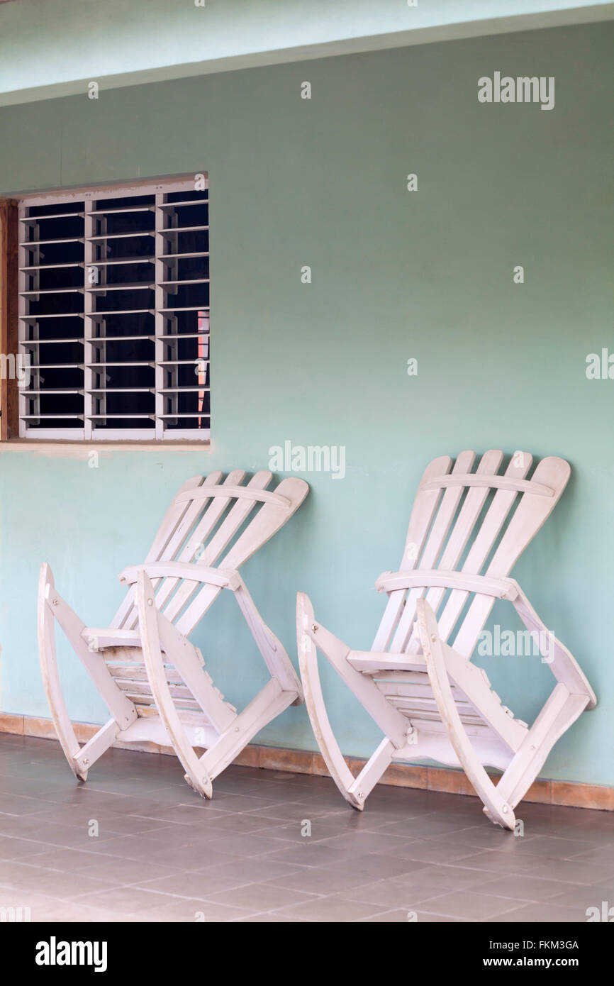 Traditional white rocking chairs lent against wall on porch of house at ...