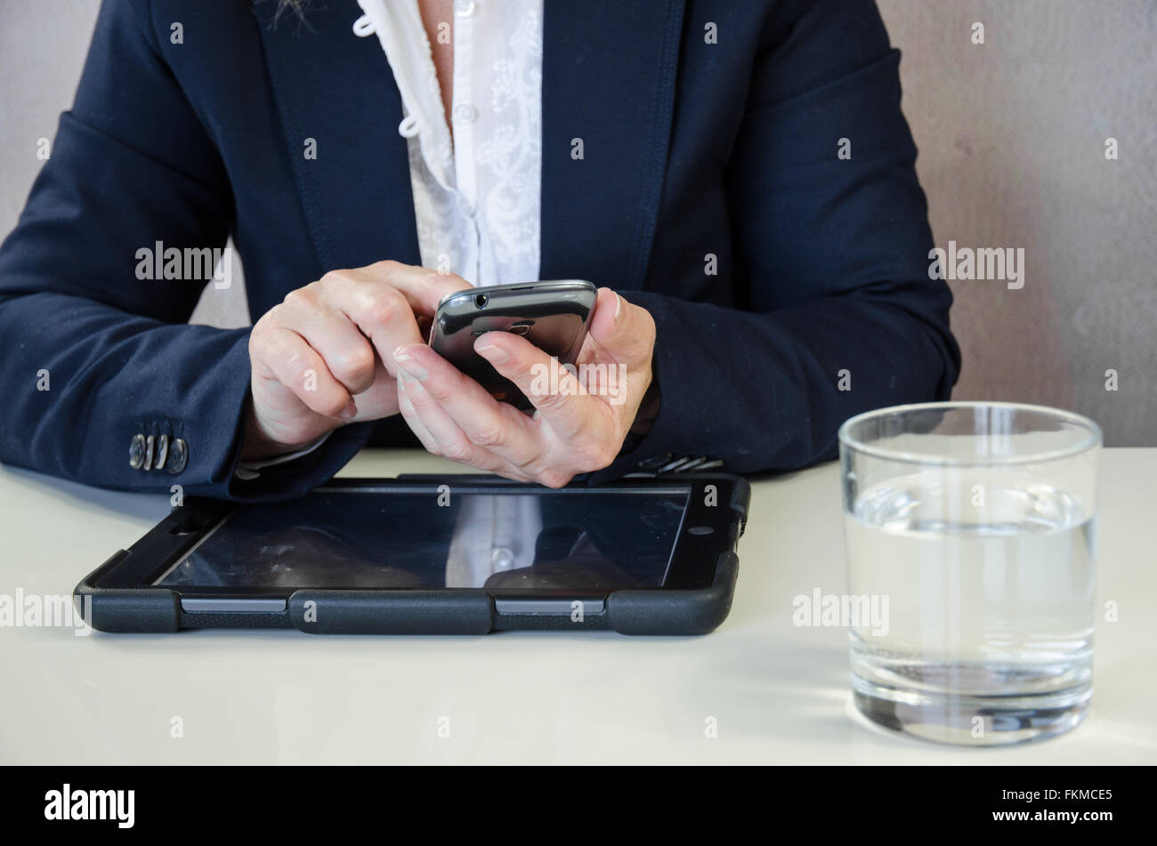 female hand typing into mobile phone behing working desk and glass of ...